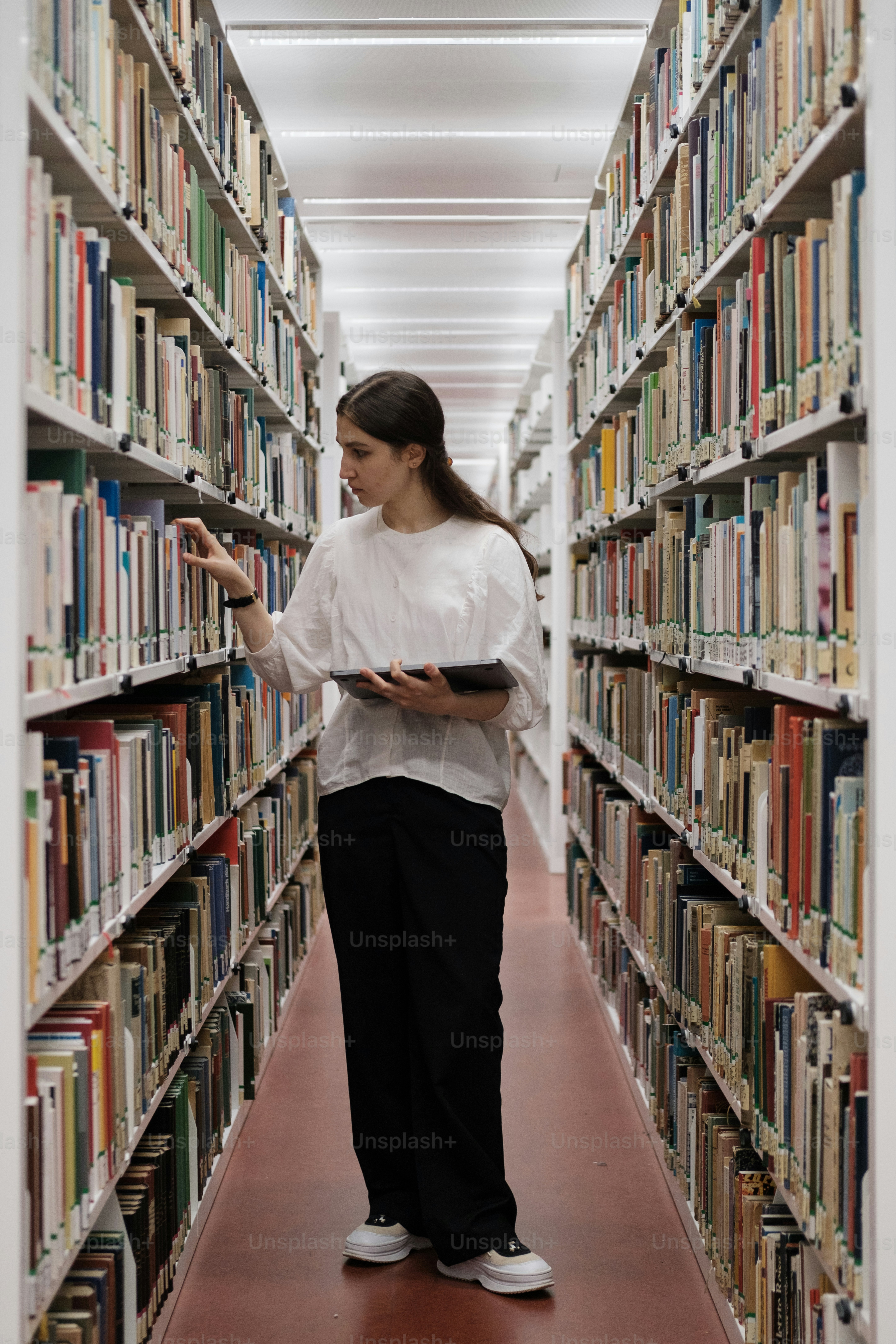 A woman holding a stack of books in a library photo – Library Image on ...