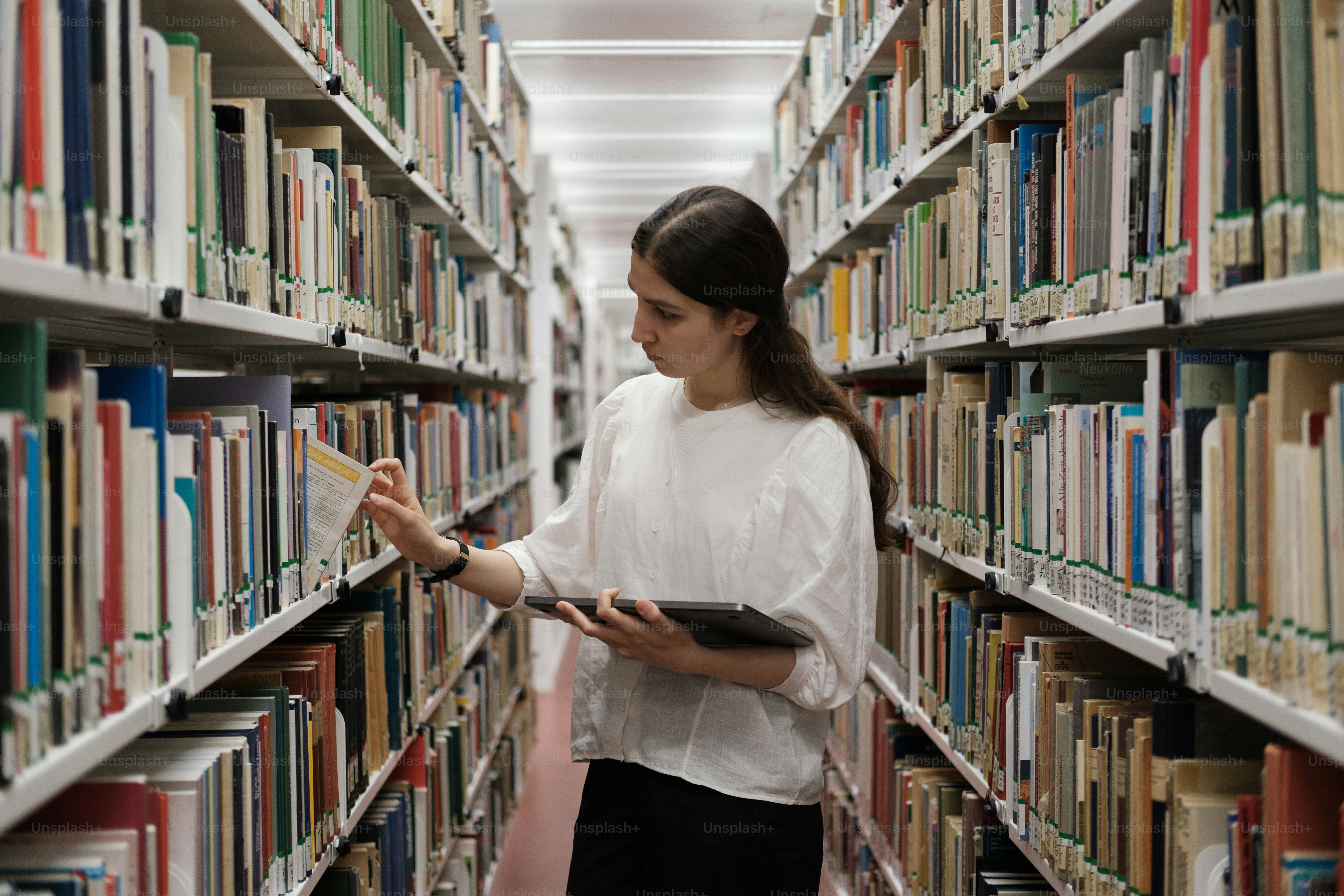 A woman standing in a library holding a book photo – Order Image on ...