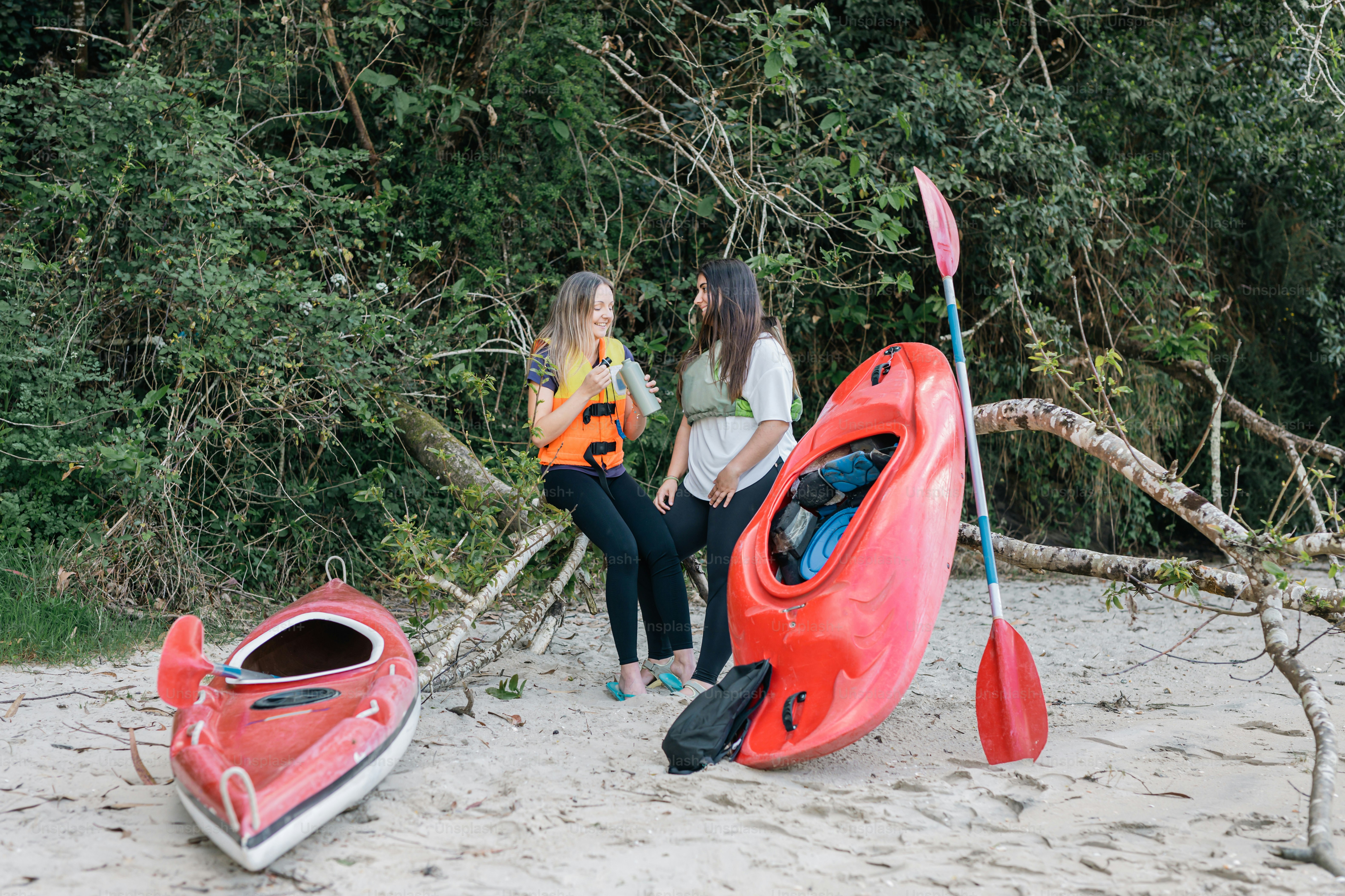 Two women standing on a beach next to kayaks photo – Canoeing Image on ...