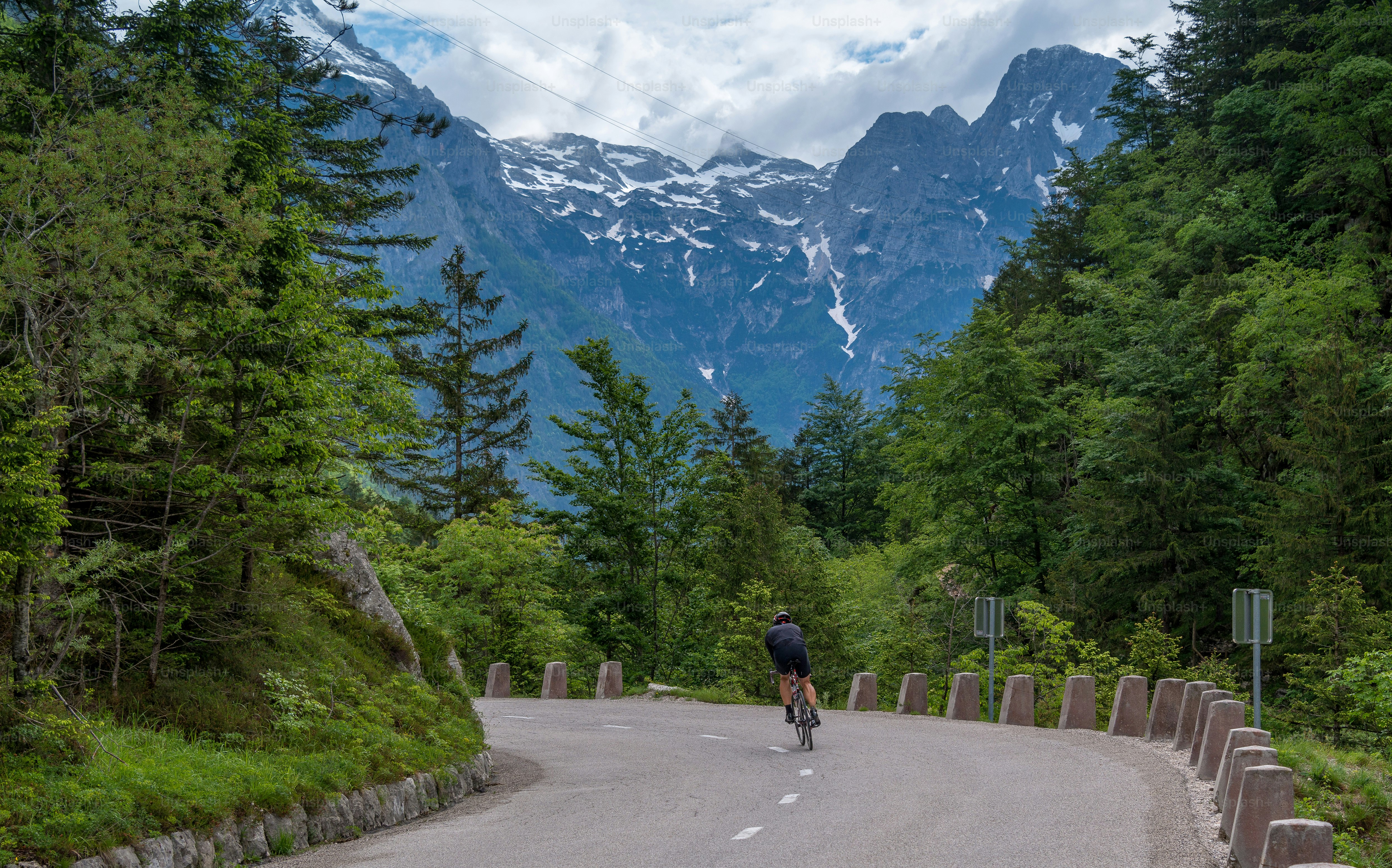 A bicyclist rides down a mountain road photo – Winding path Image on ...
