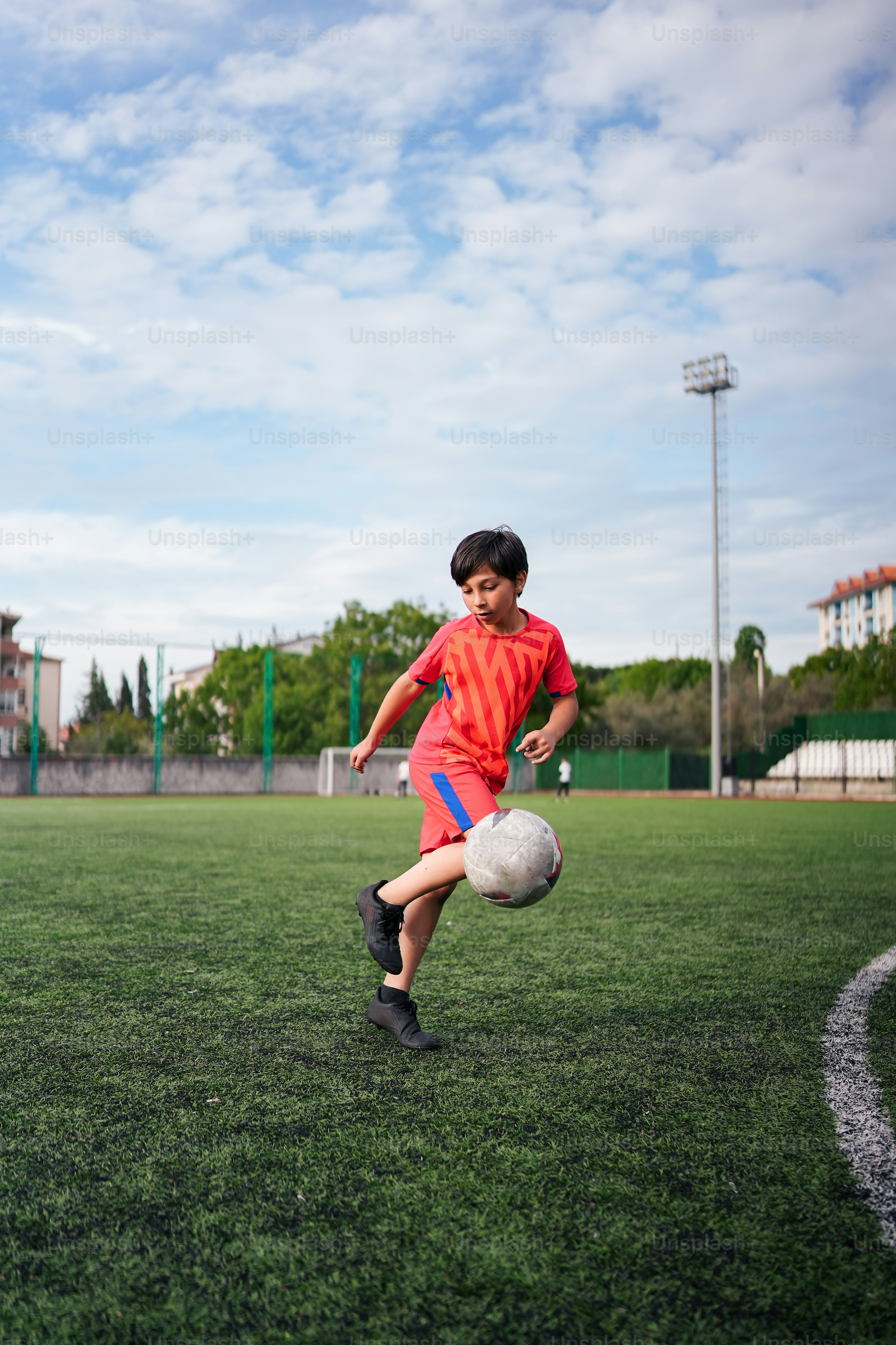 Un jeune garçon tapant dans un ballon de football sur un terrain photo ...