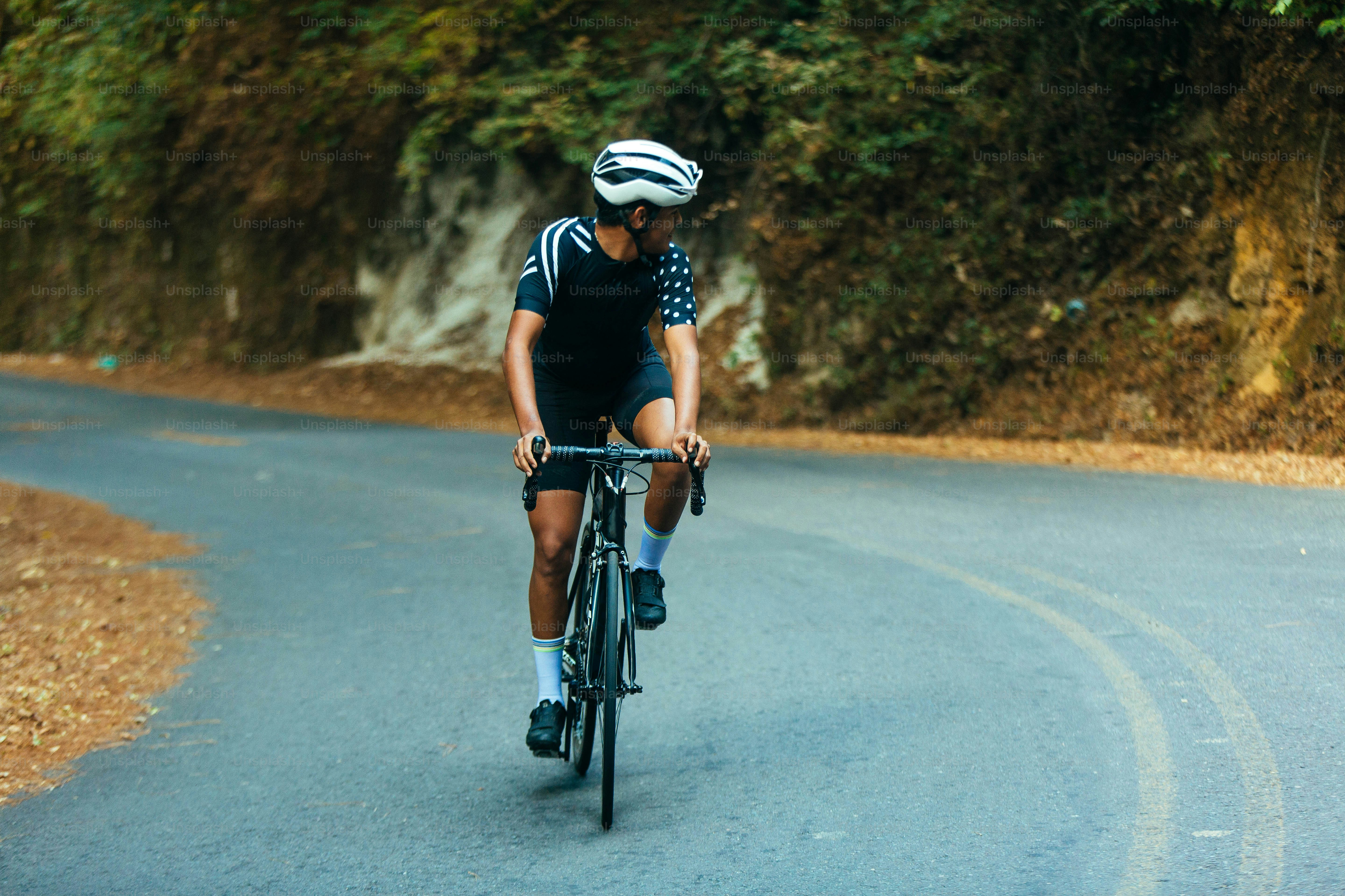 A man riding a bike down a road next to a forest photo – Sport Image on ...