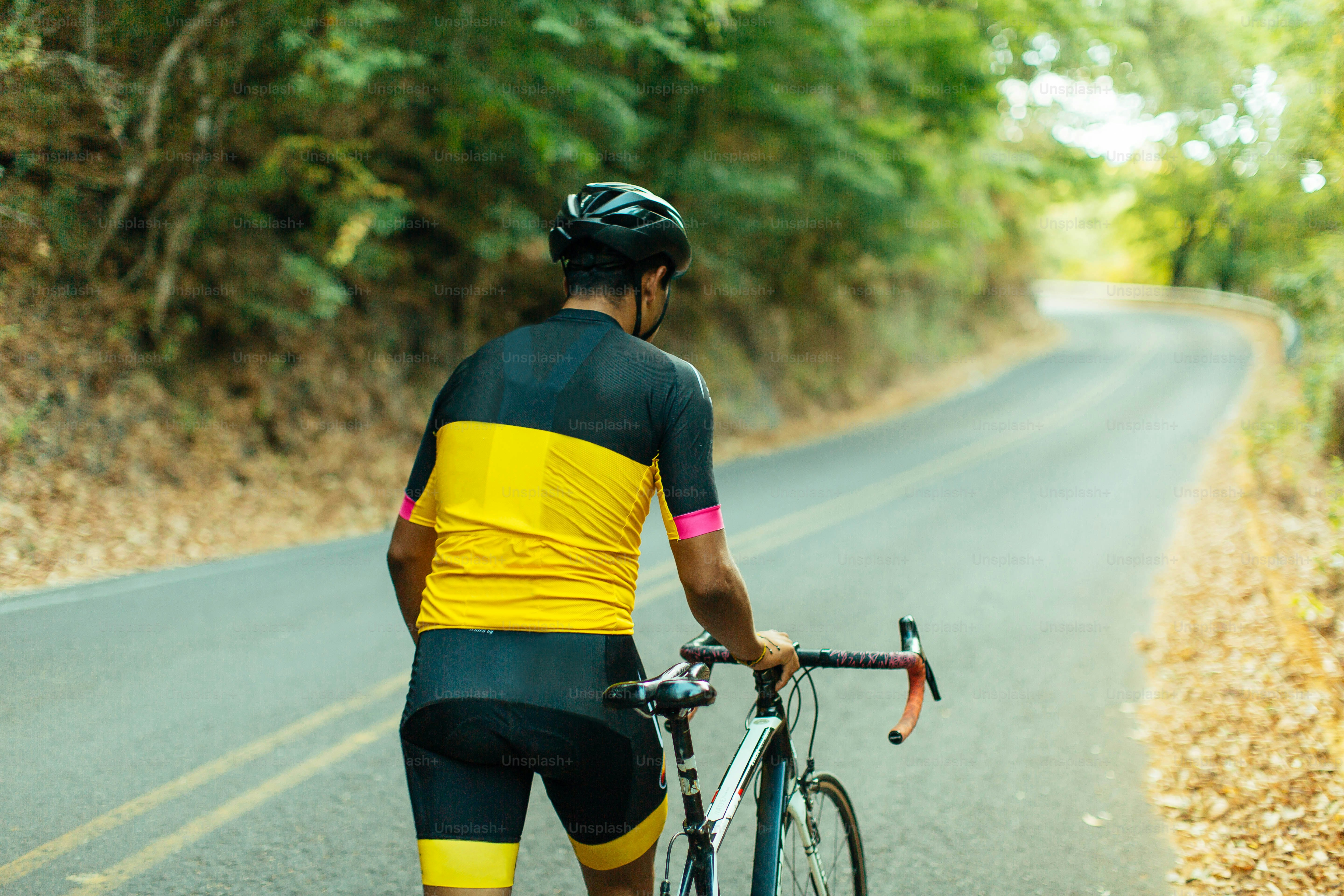 A man riding a bike down a road next to a forest photo – Sport Image on ...