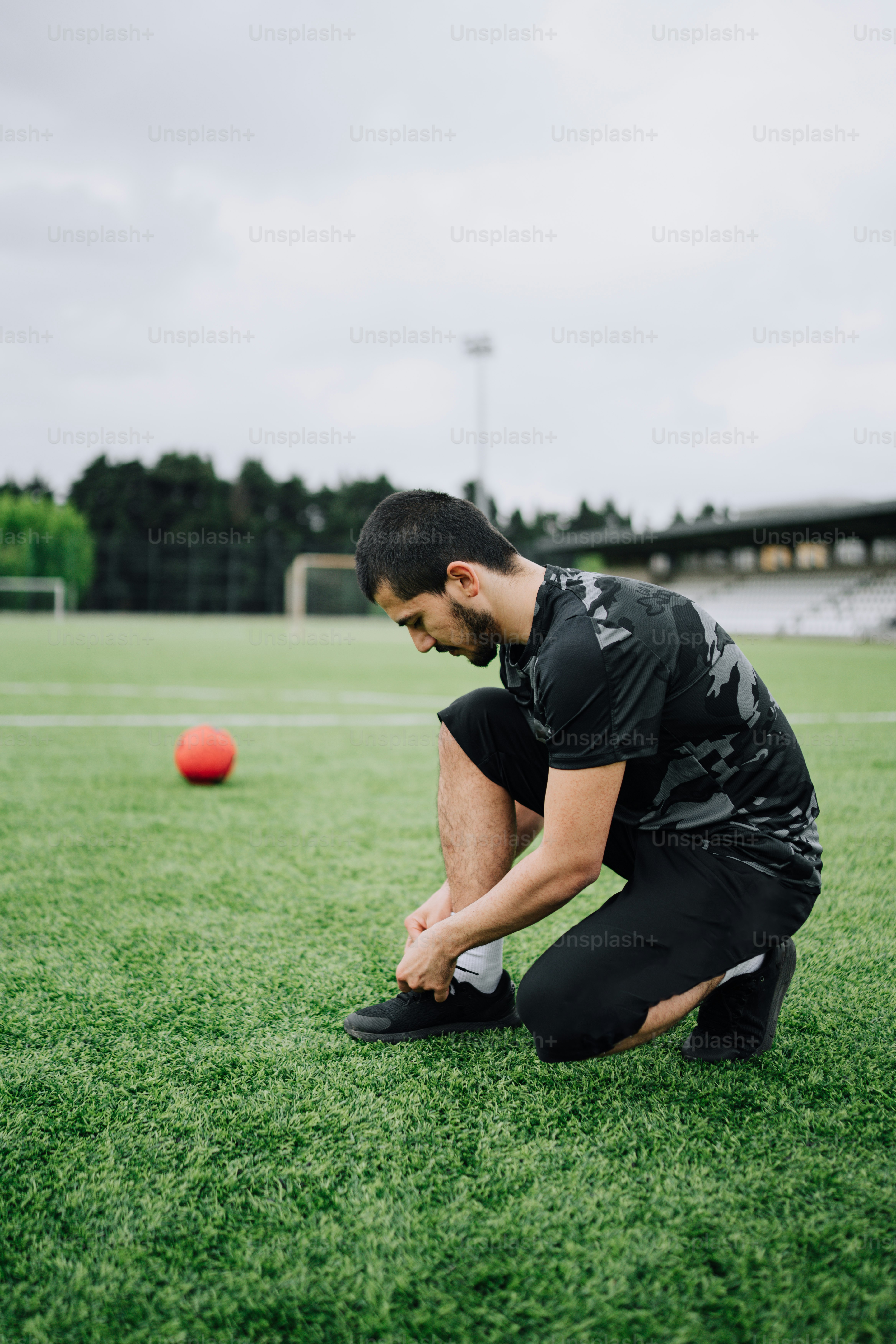 A man kneeling down on top of a lush green field photo – Football boots ...