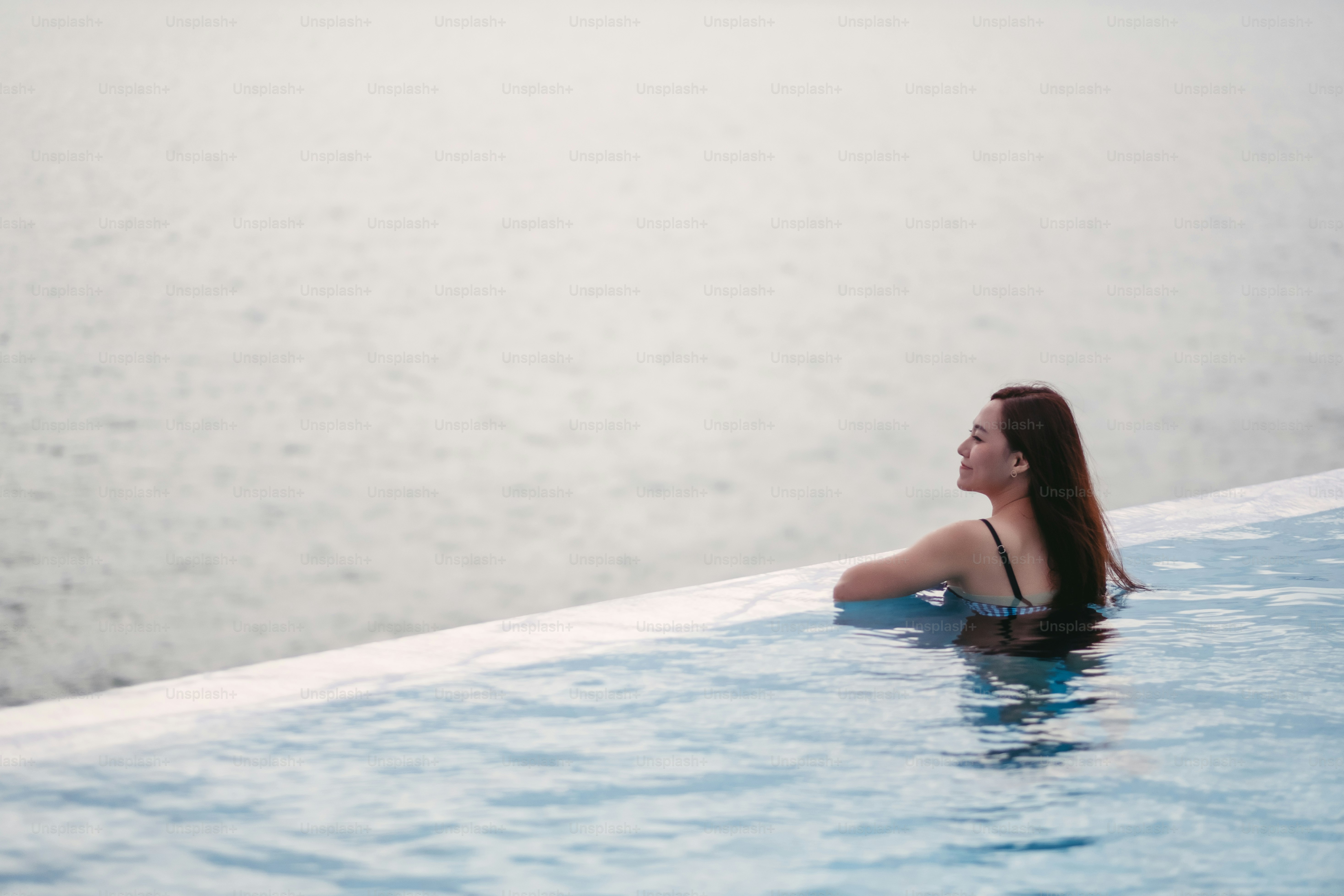 A young asian woman relaxing in infinity swimming pool looking at a beautiful sea view foto ...