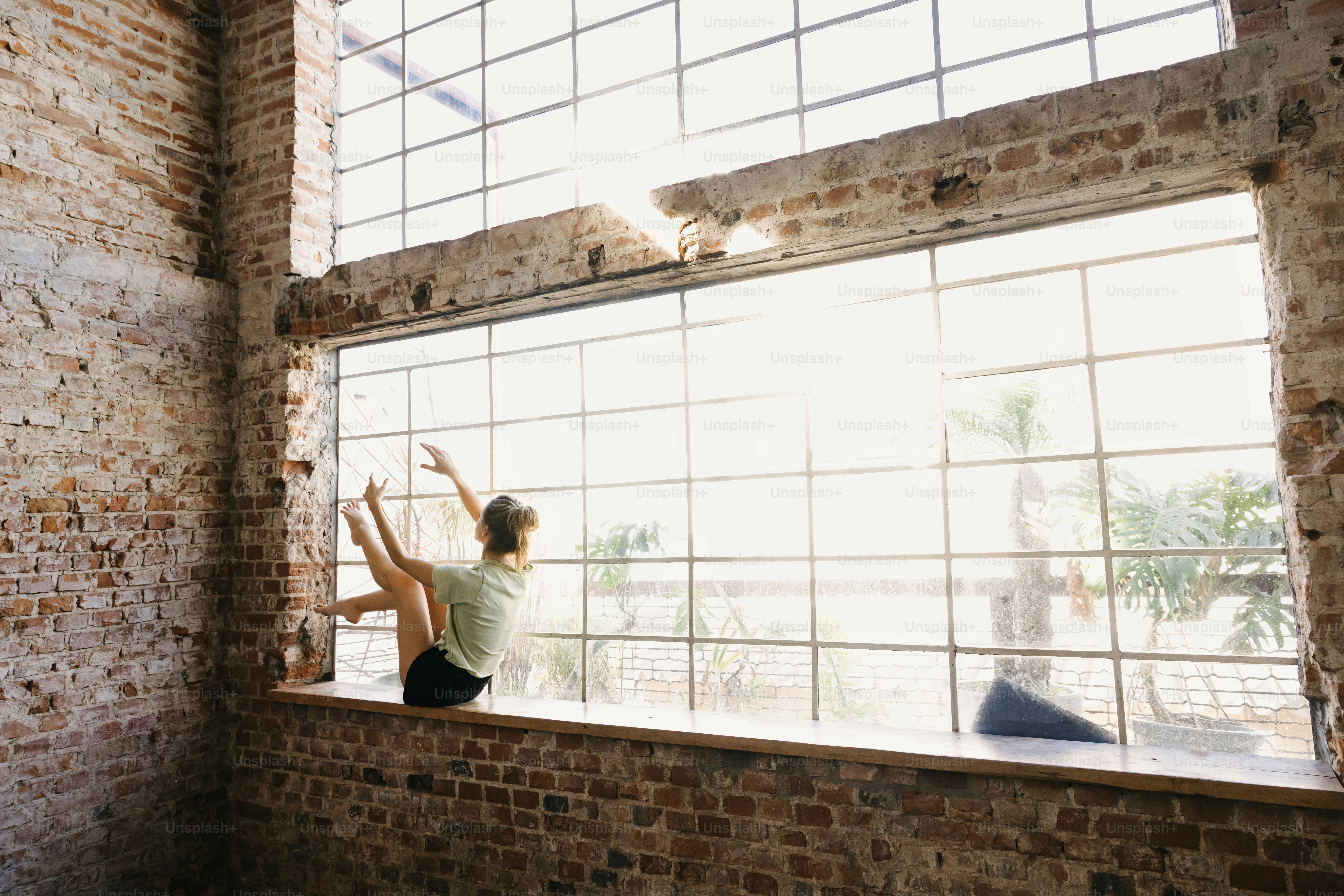 A woman standing on a window sill in front of a brick wall photo ...