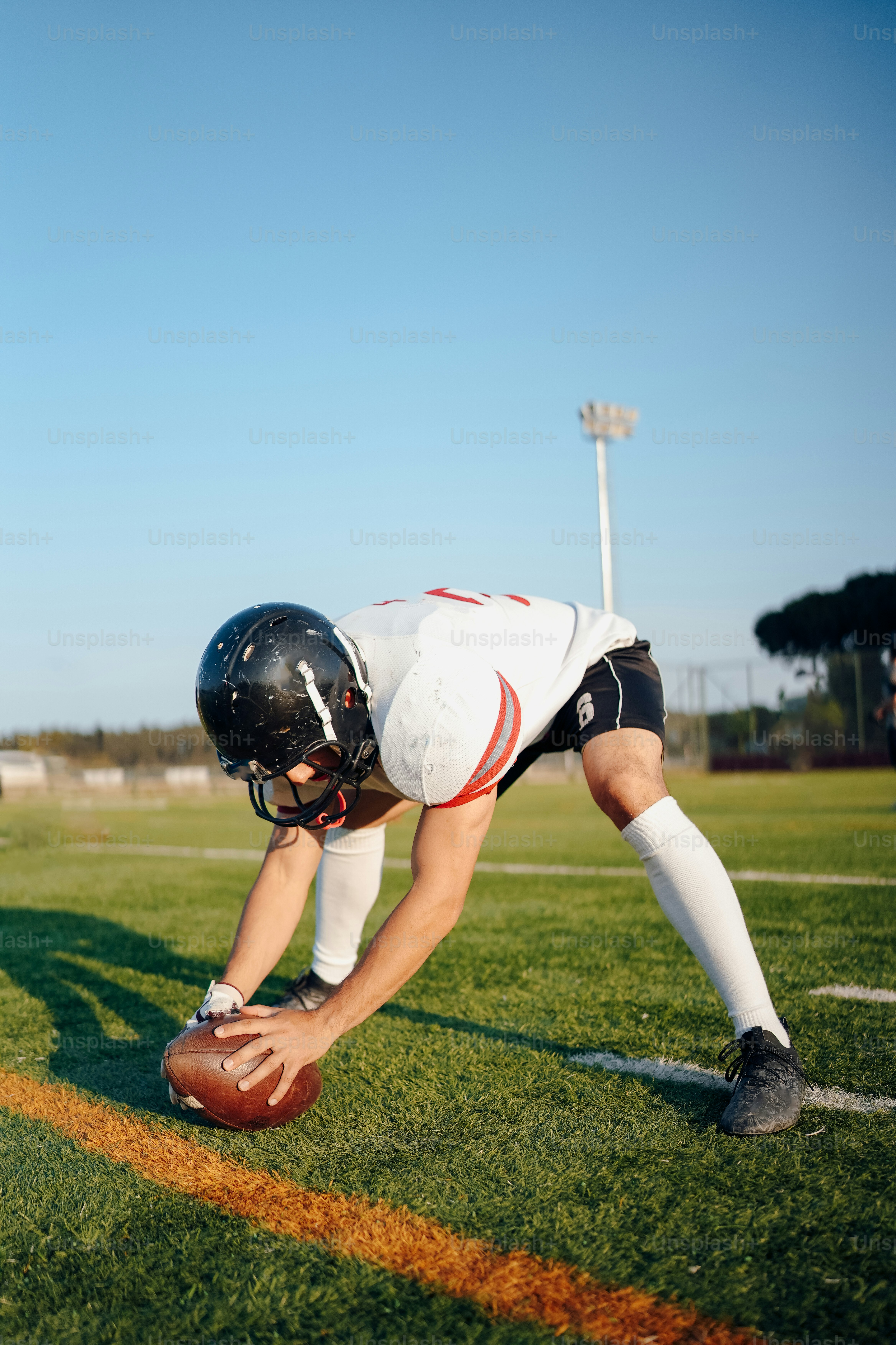 A football player kneeling down to pick up a ball photo – Athletics ...
