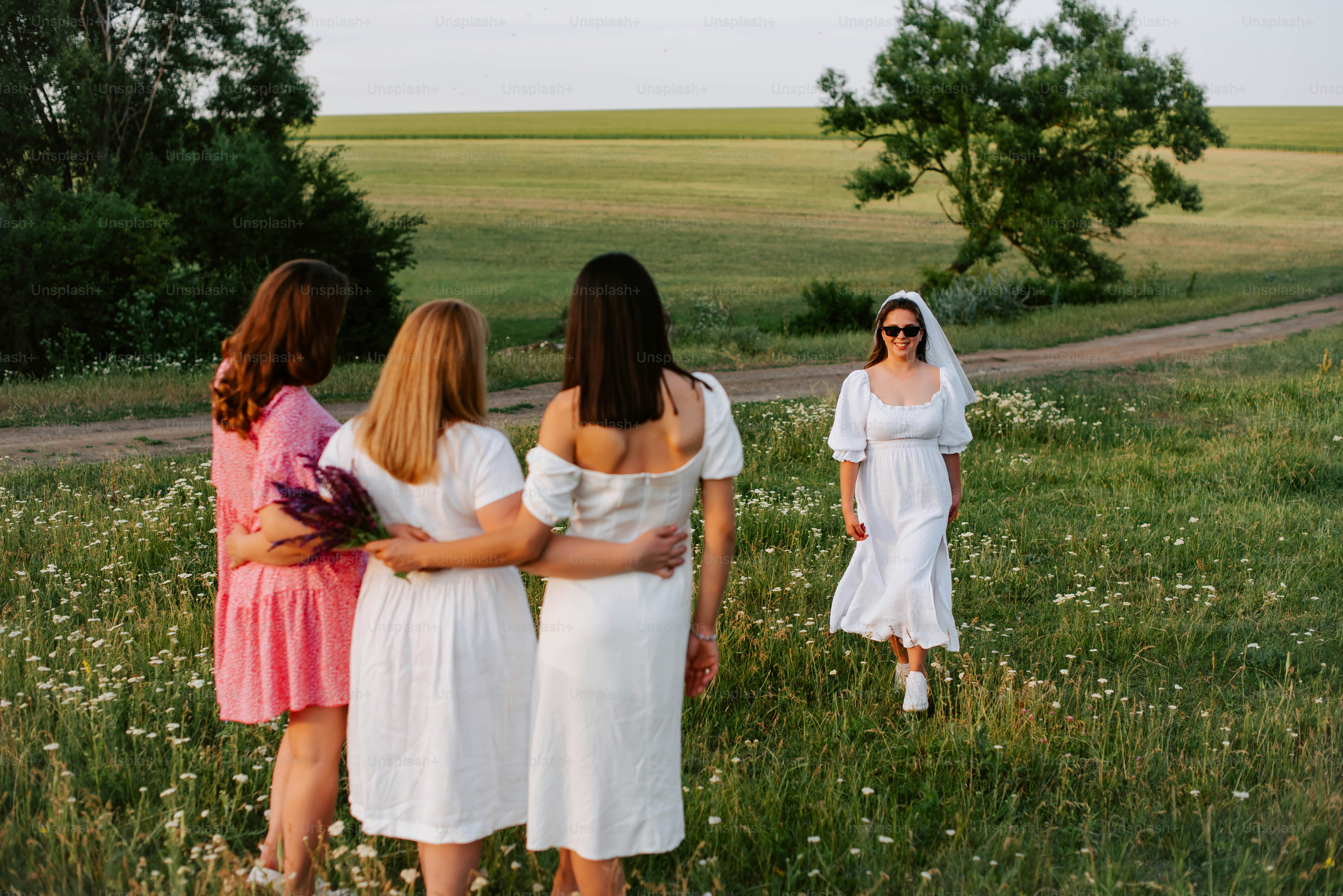 A group of women in white dresses standing in a field photo – Bridal ...