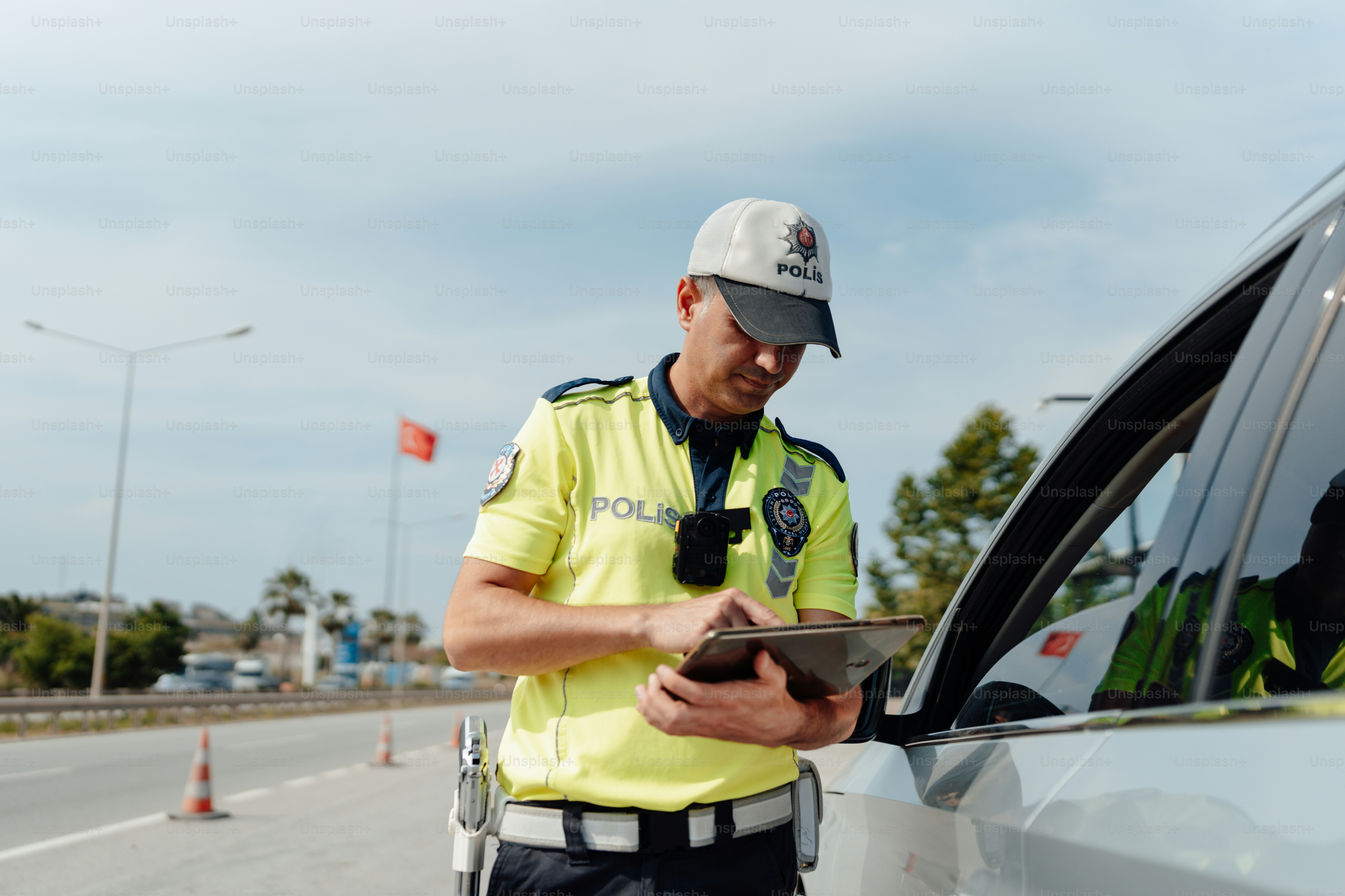 A police officer standing next to a car holding a tablet photo ...