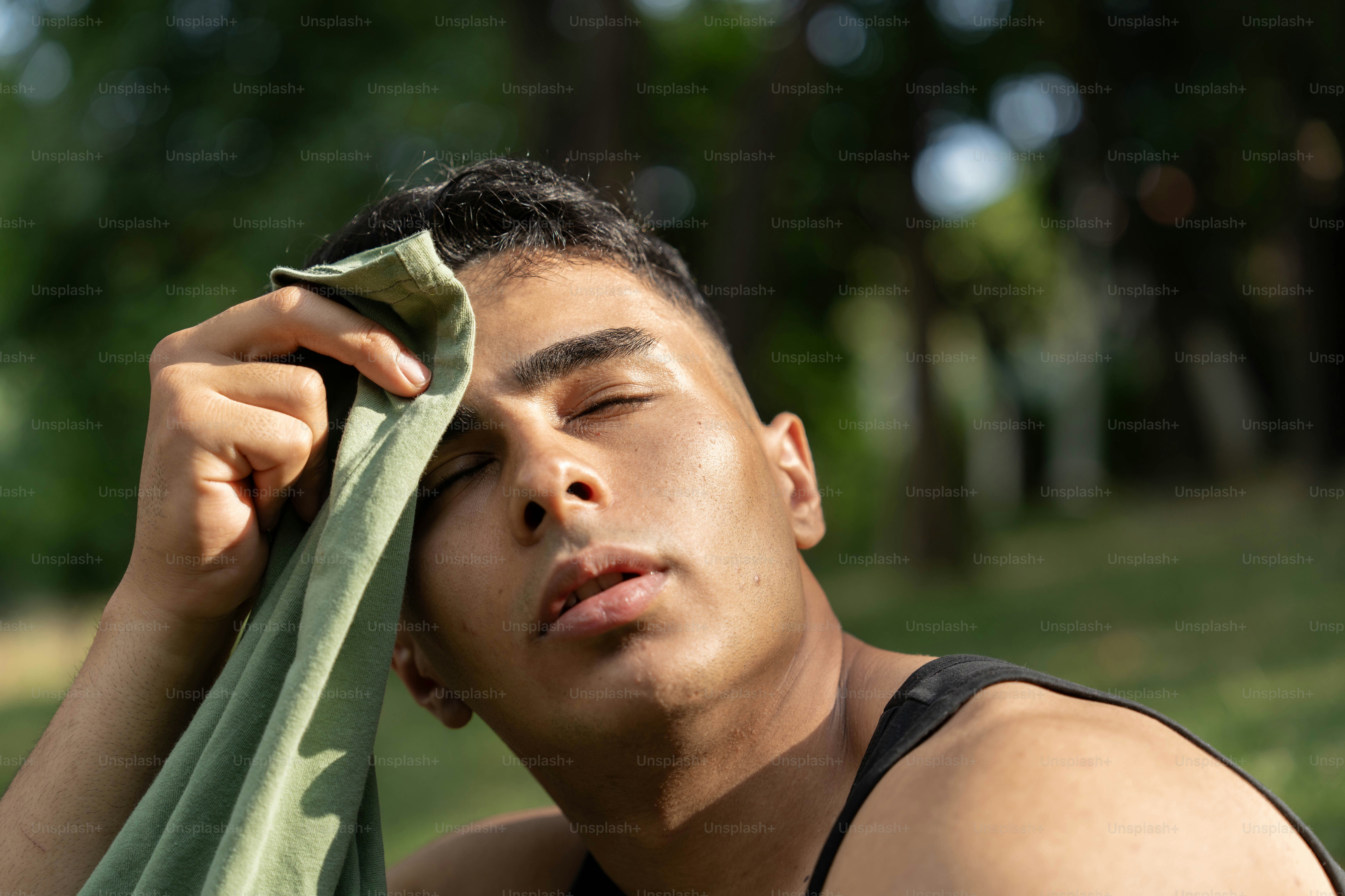 A man holding a green cloth over his eyes photo – Sweating Image on ...