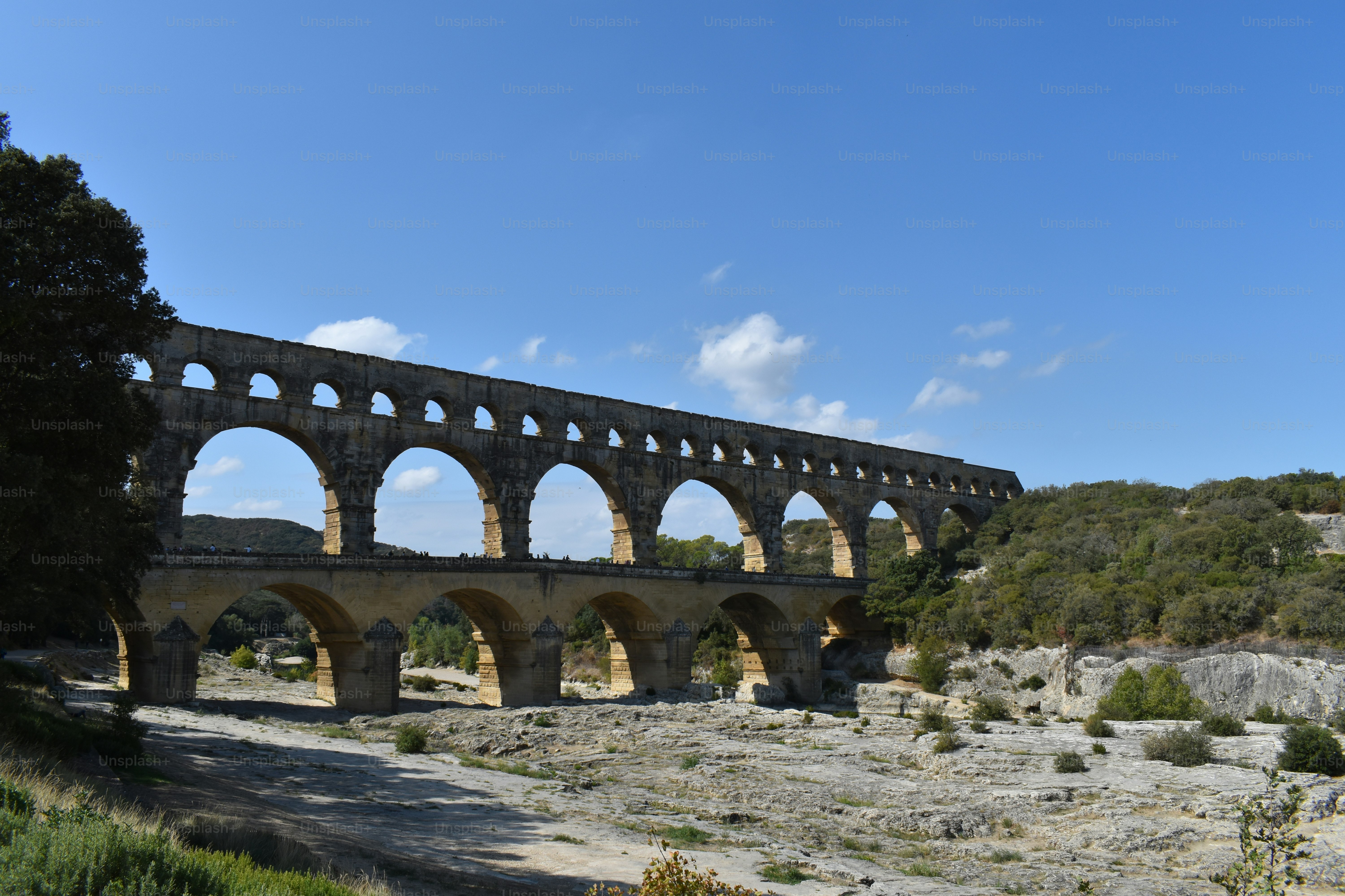 A stone bridge over a river surrounded by trees photo – Pont du gard ...
