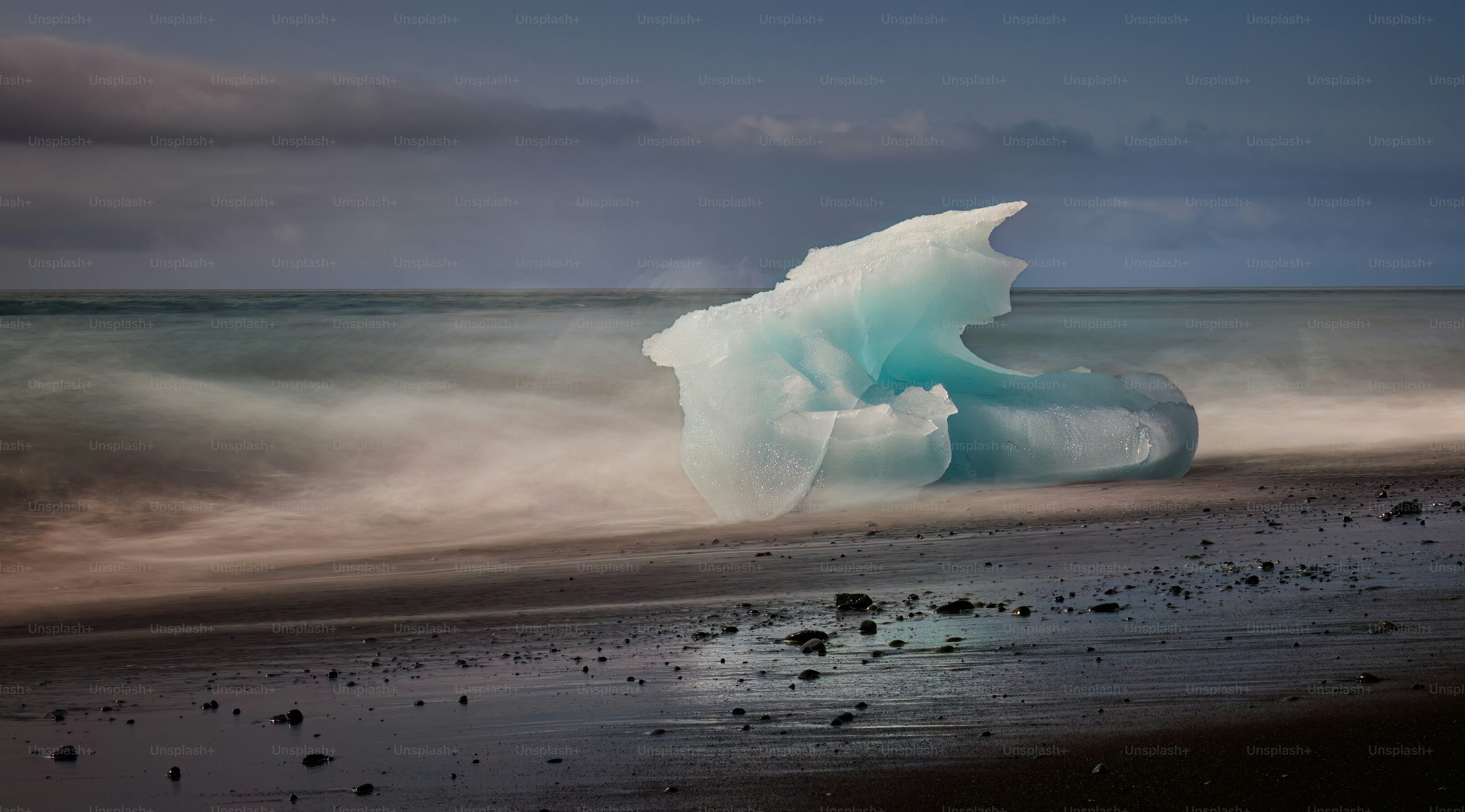 A large iceberg floating on top of a sandy beach photo – Wallpaper ...