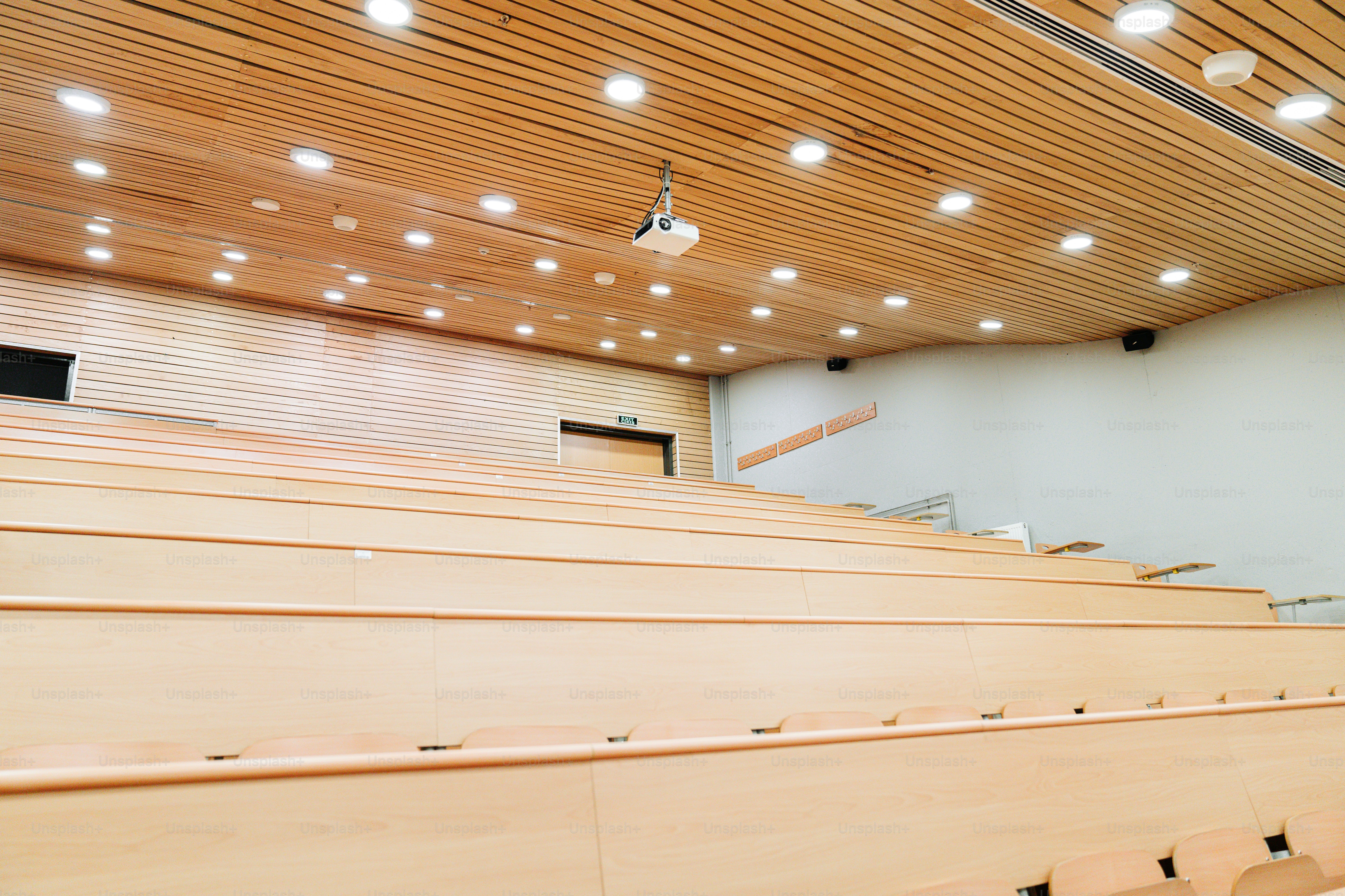 A lecture hall with wooden seats and a projector screen photo – College ...