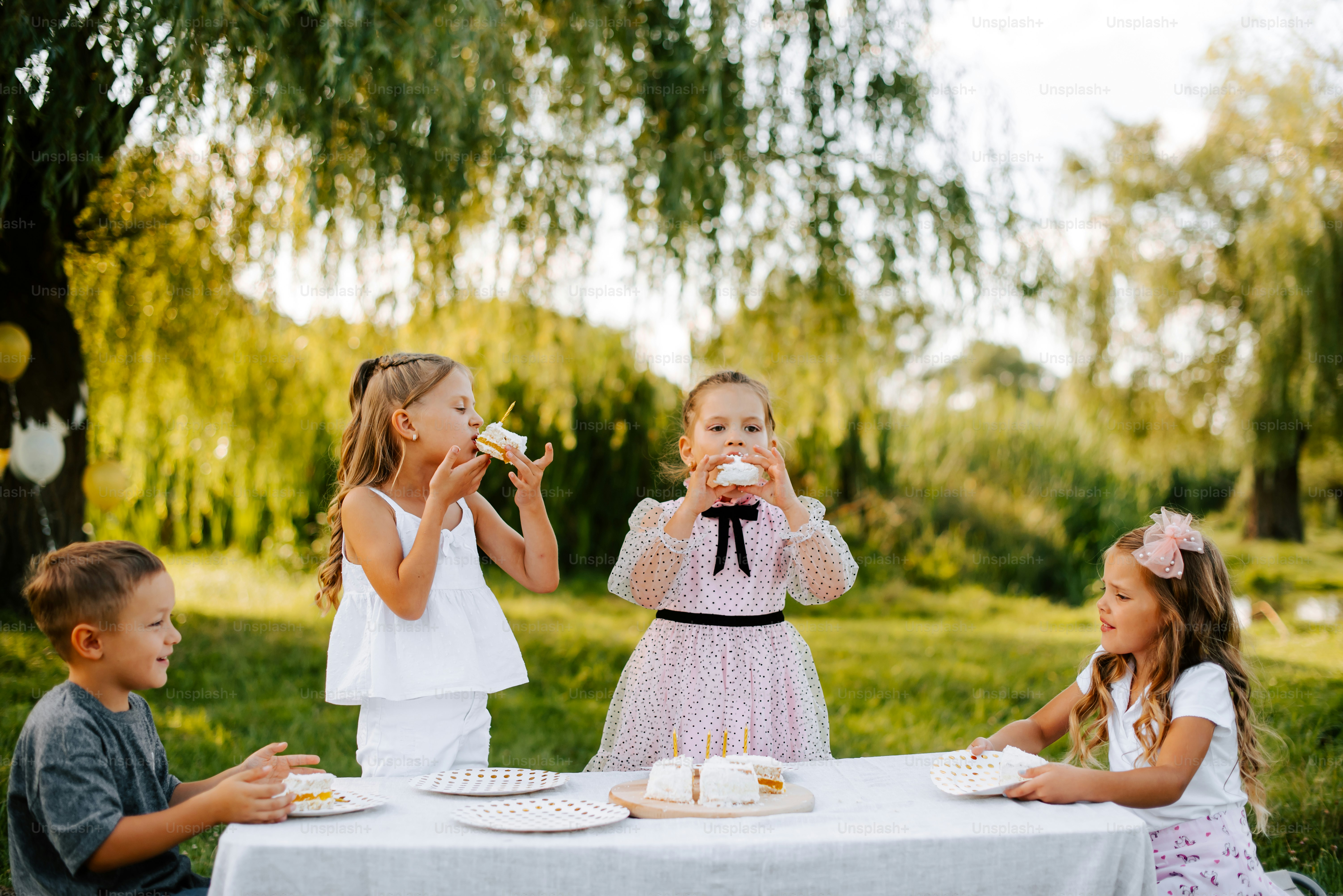 A group of children sitting around a table eating cake photo – Birthday ...