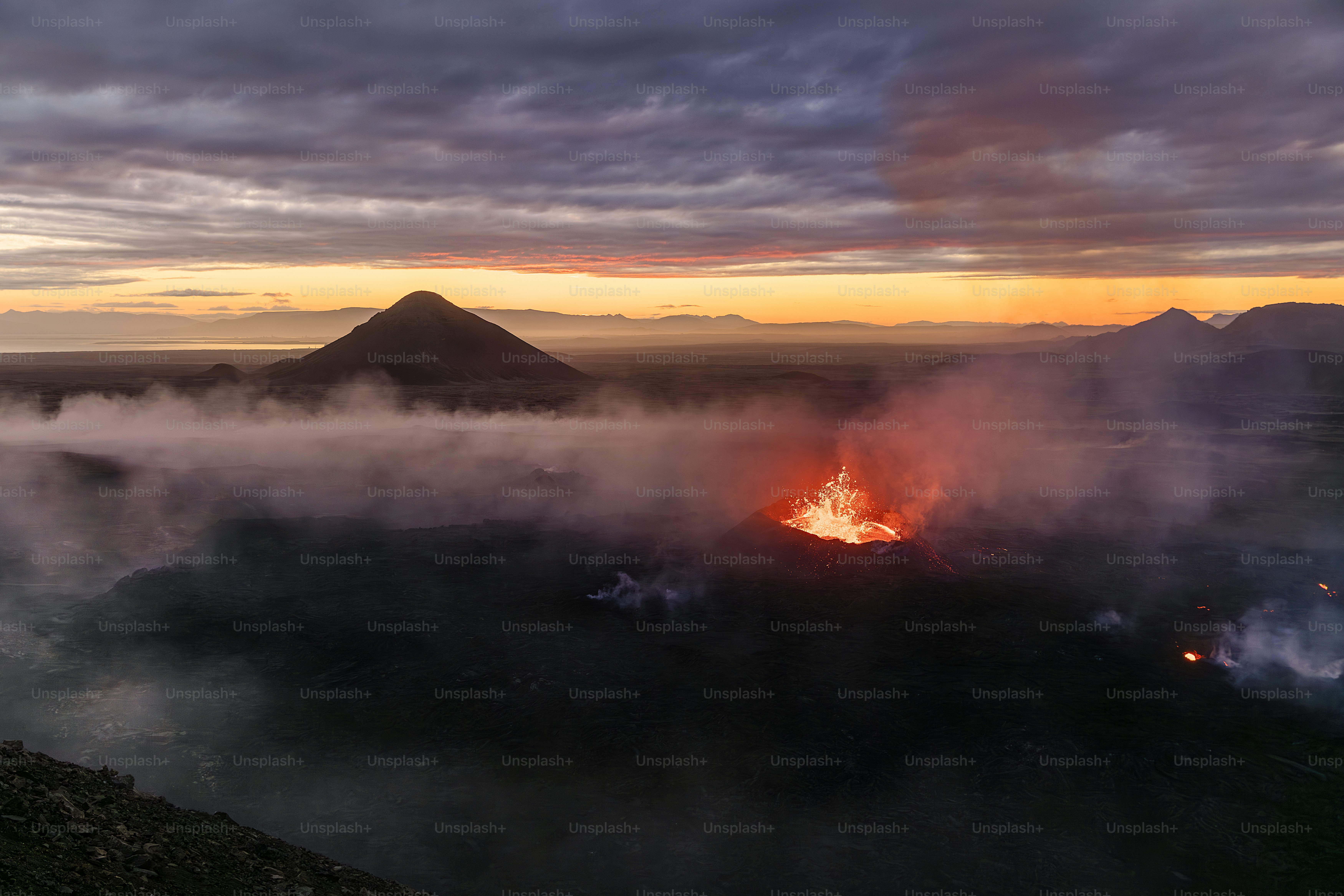 A volcano spewing out lava in the middle of a valley photo – Sunset ...