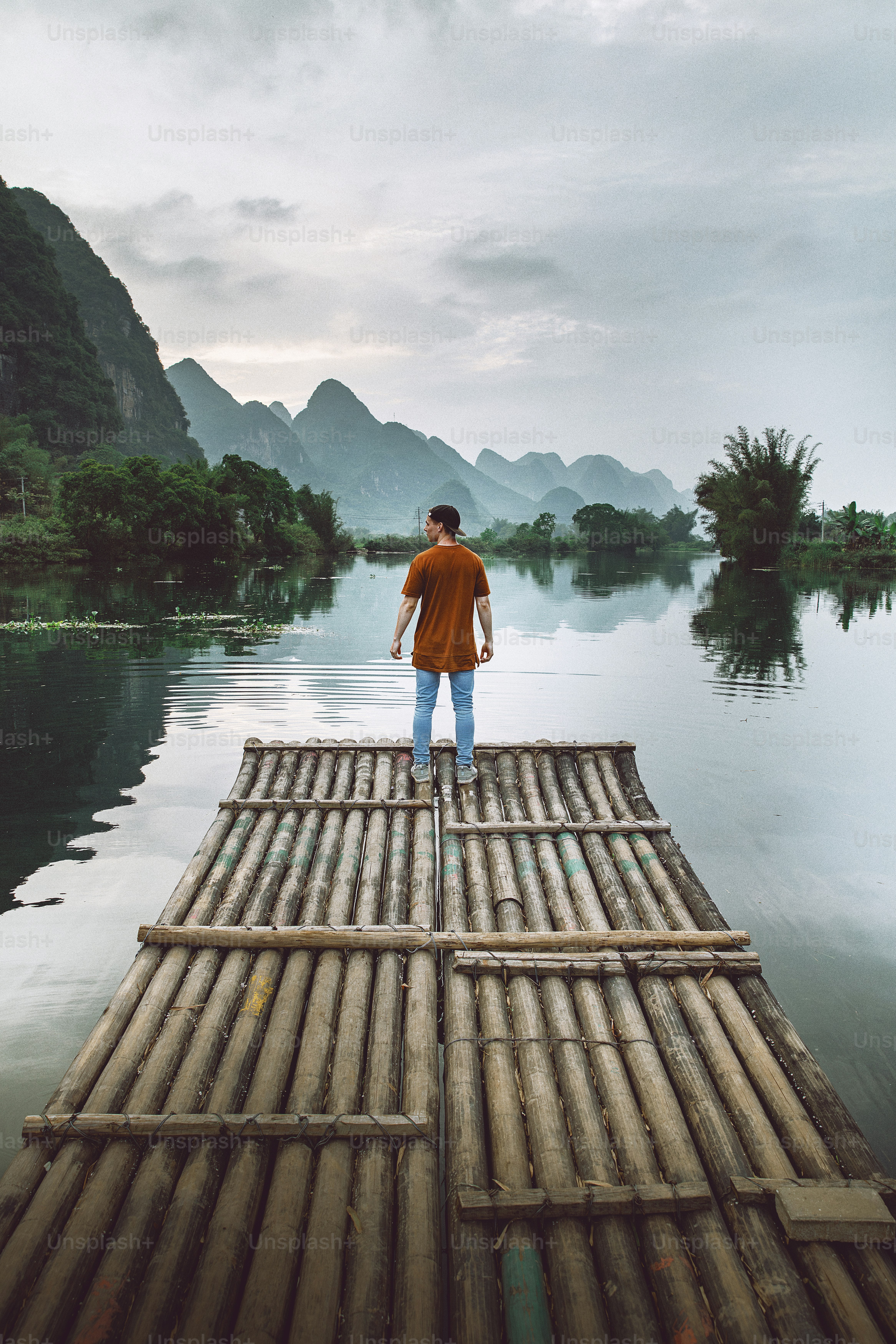 A person standing on a bamboo raft in the middle of a body of water ...