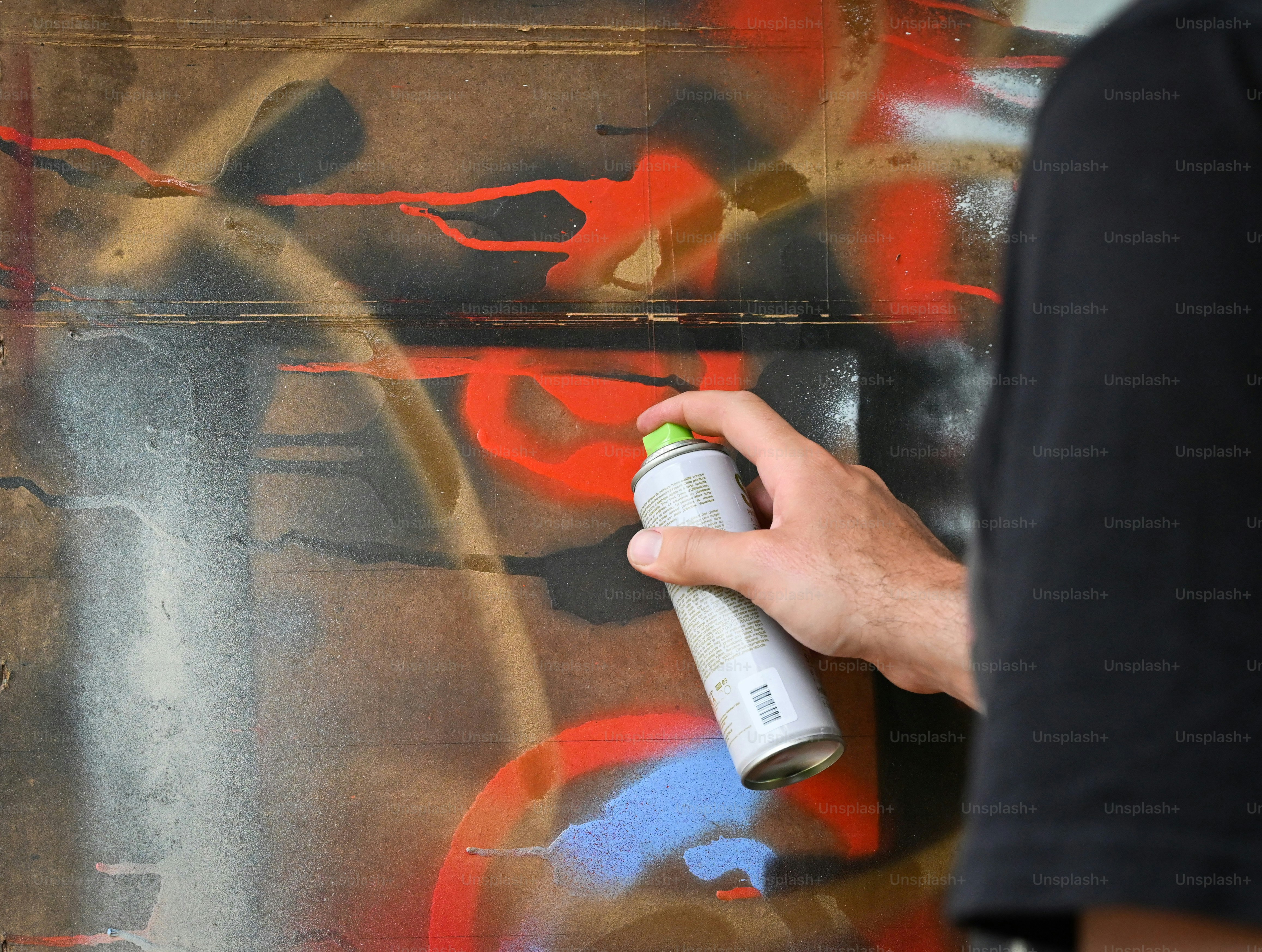 A person spray painting a wall with graffiti photo – Street art Image ...