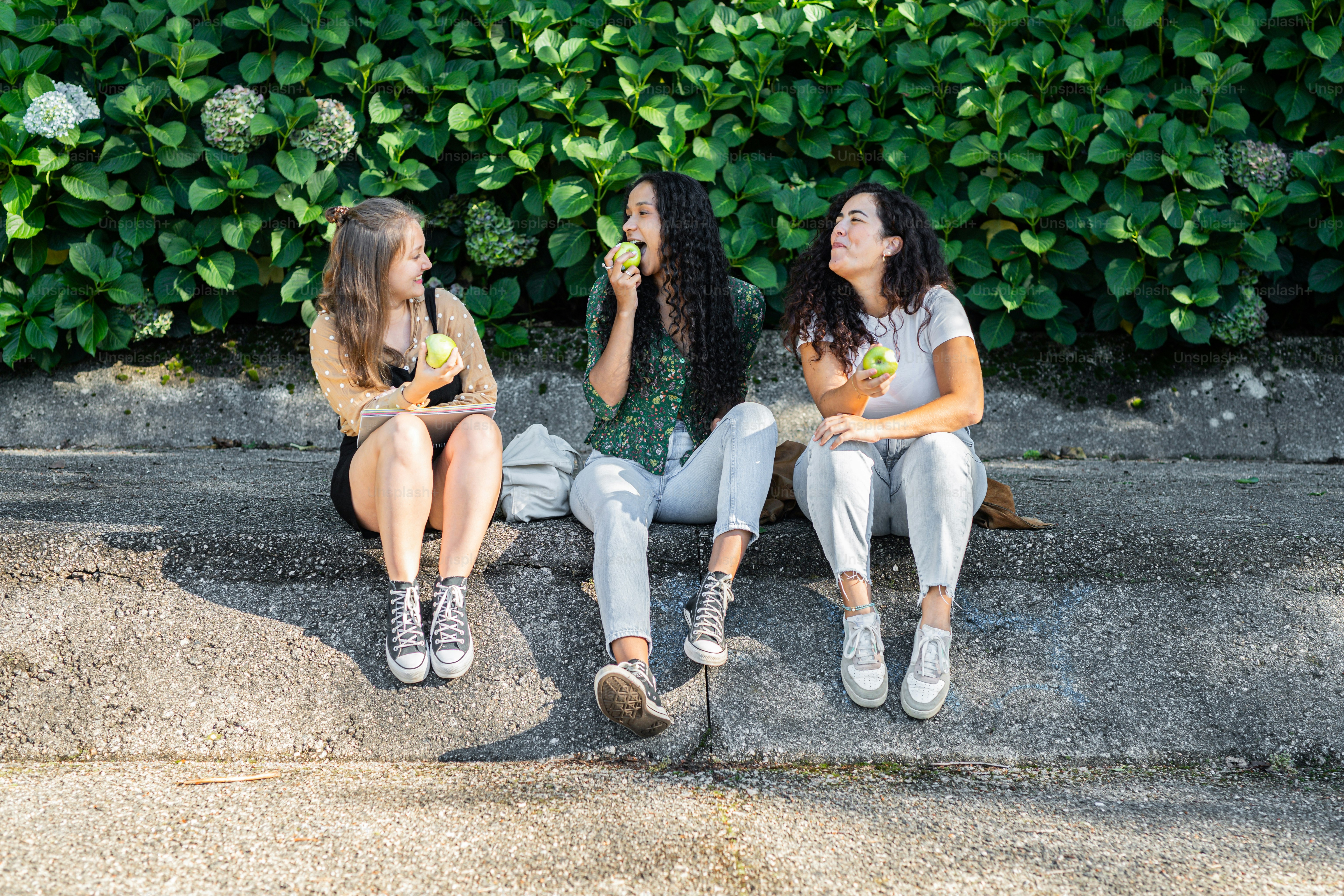 Three girls sitting on a curb eating and drinking photo – College Image ...