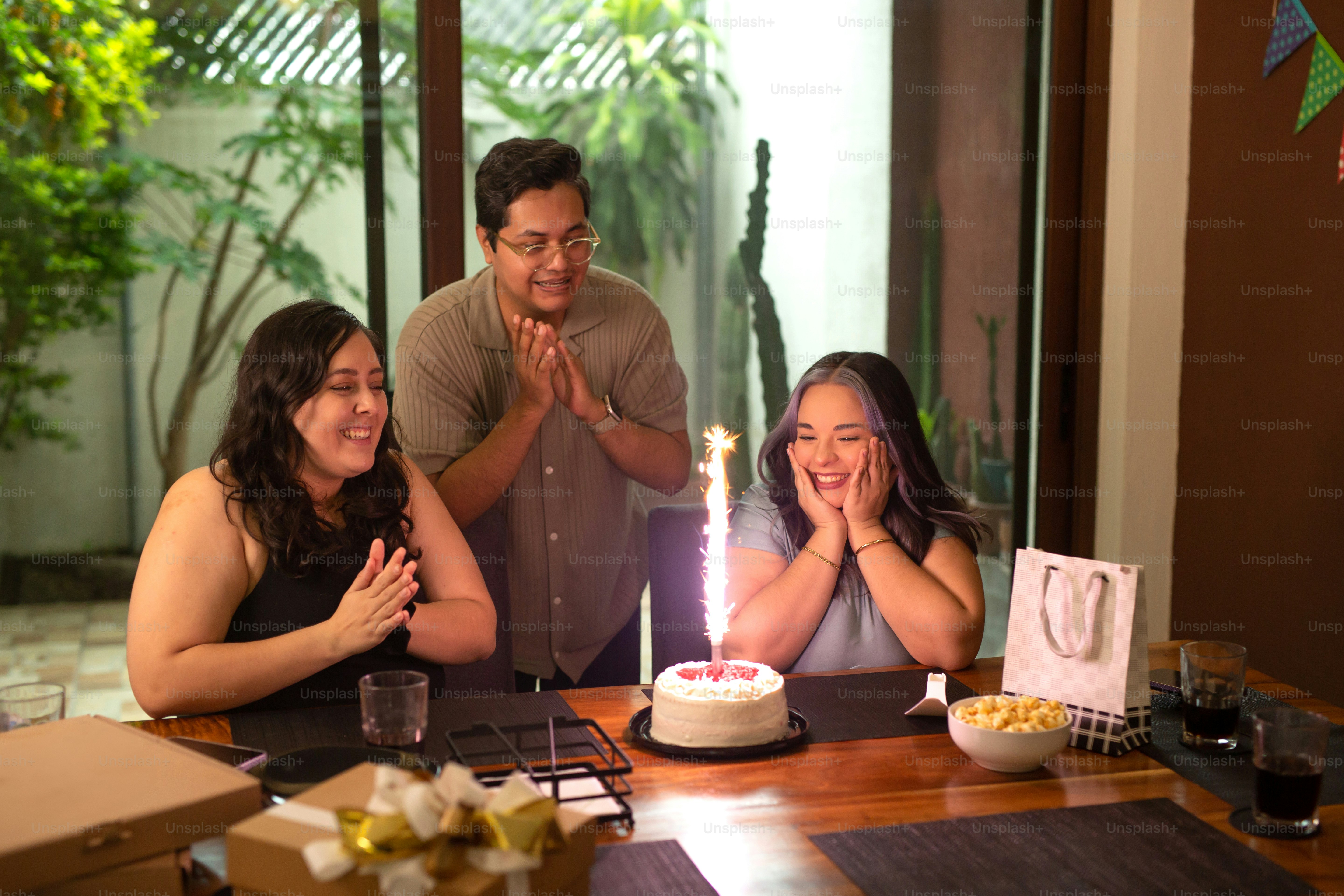 A group of people sitting around a table with a cake photo – Birthday ...