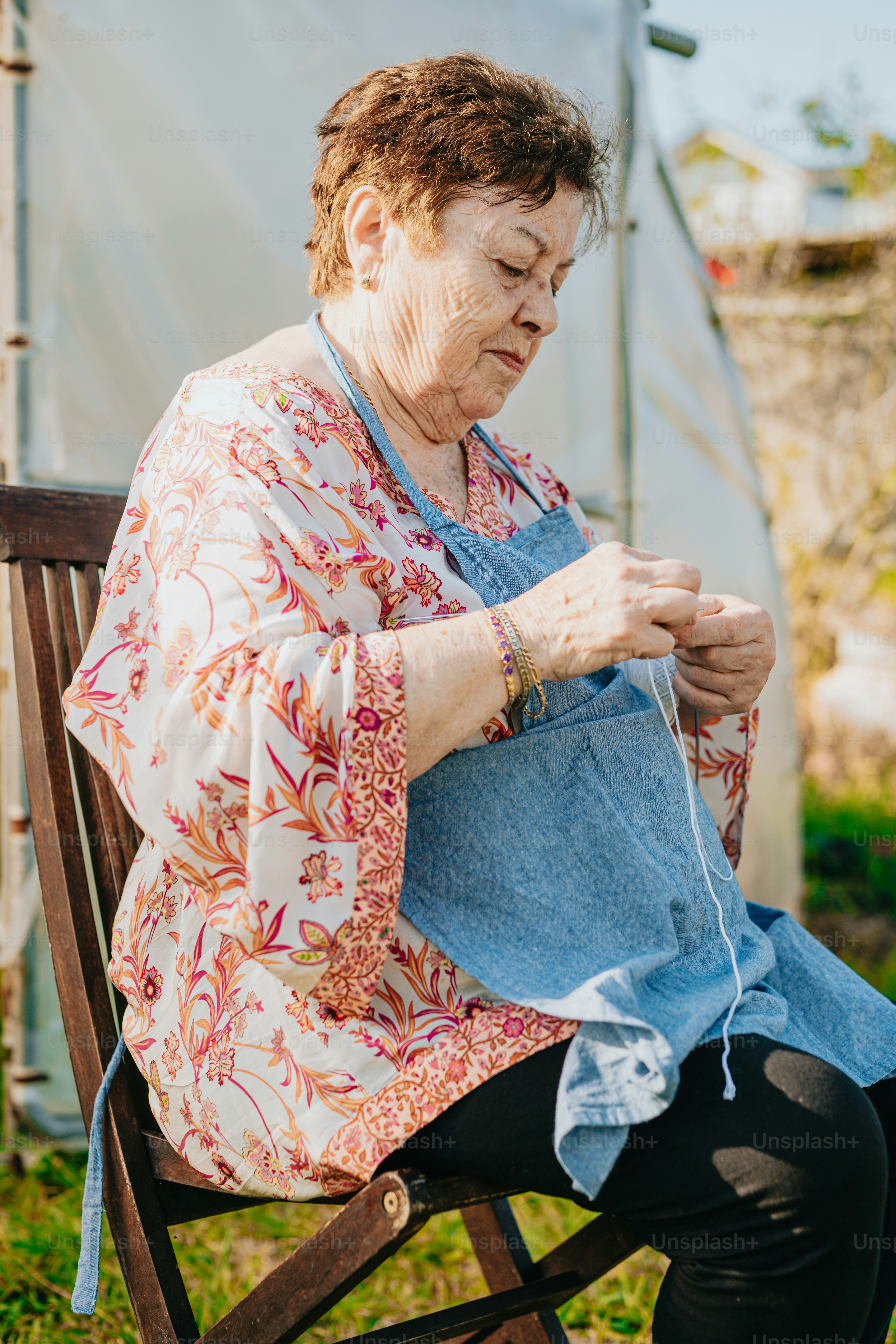 A woman sitting on a chair knitting a piece of cloth photo – Elderly ...