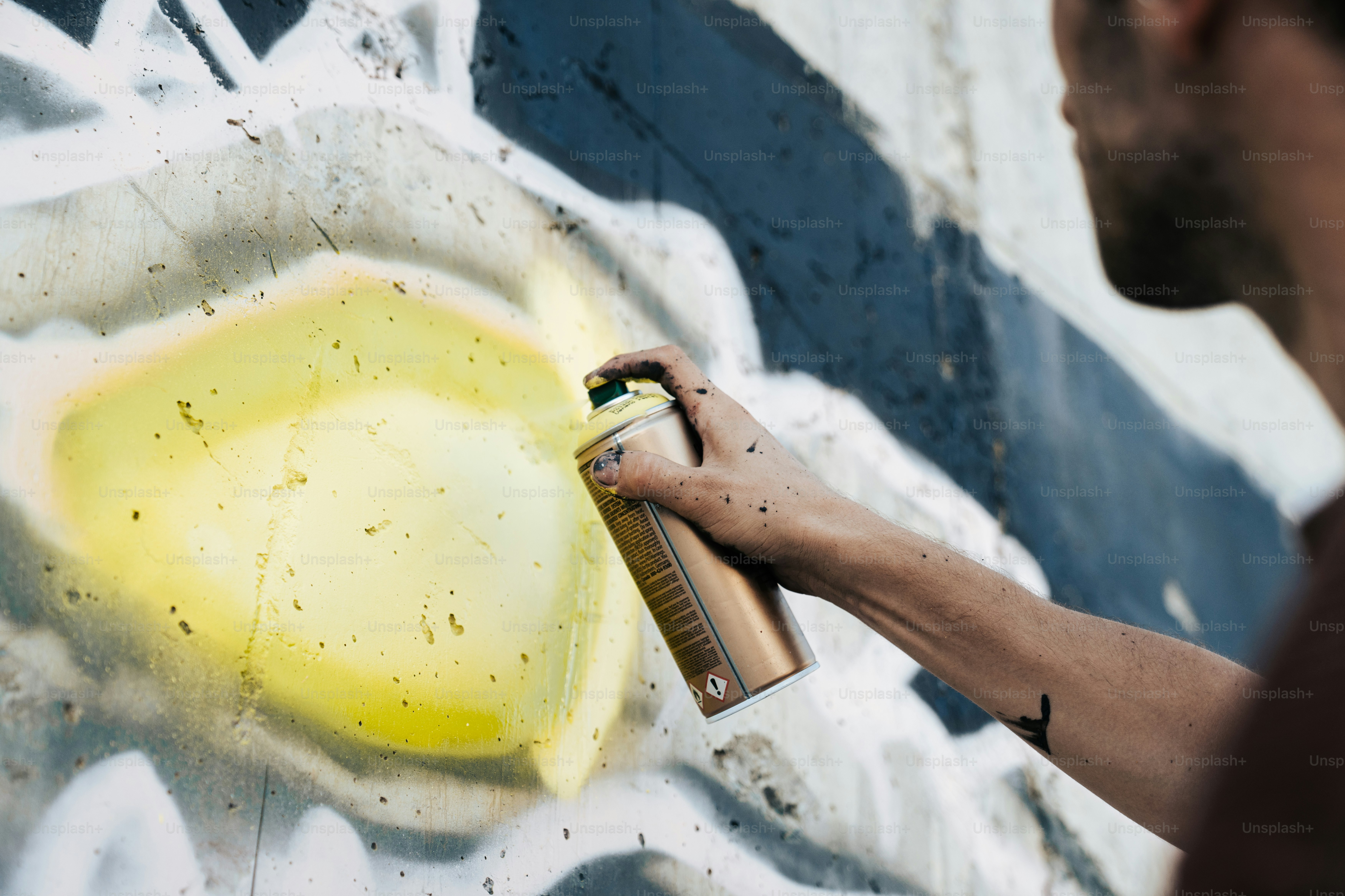 A man spray painting a wall with yellow paint photo – Street art Image ...