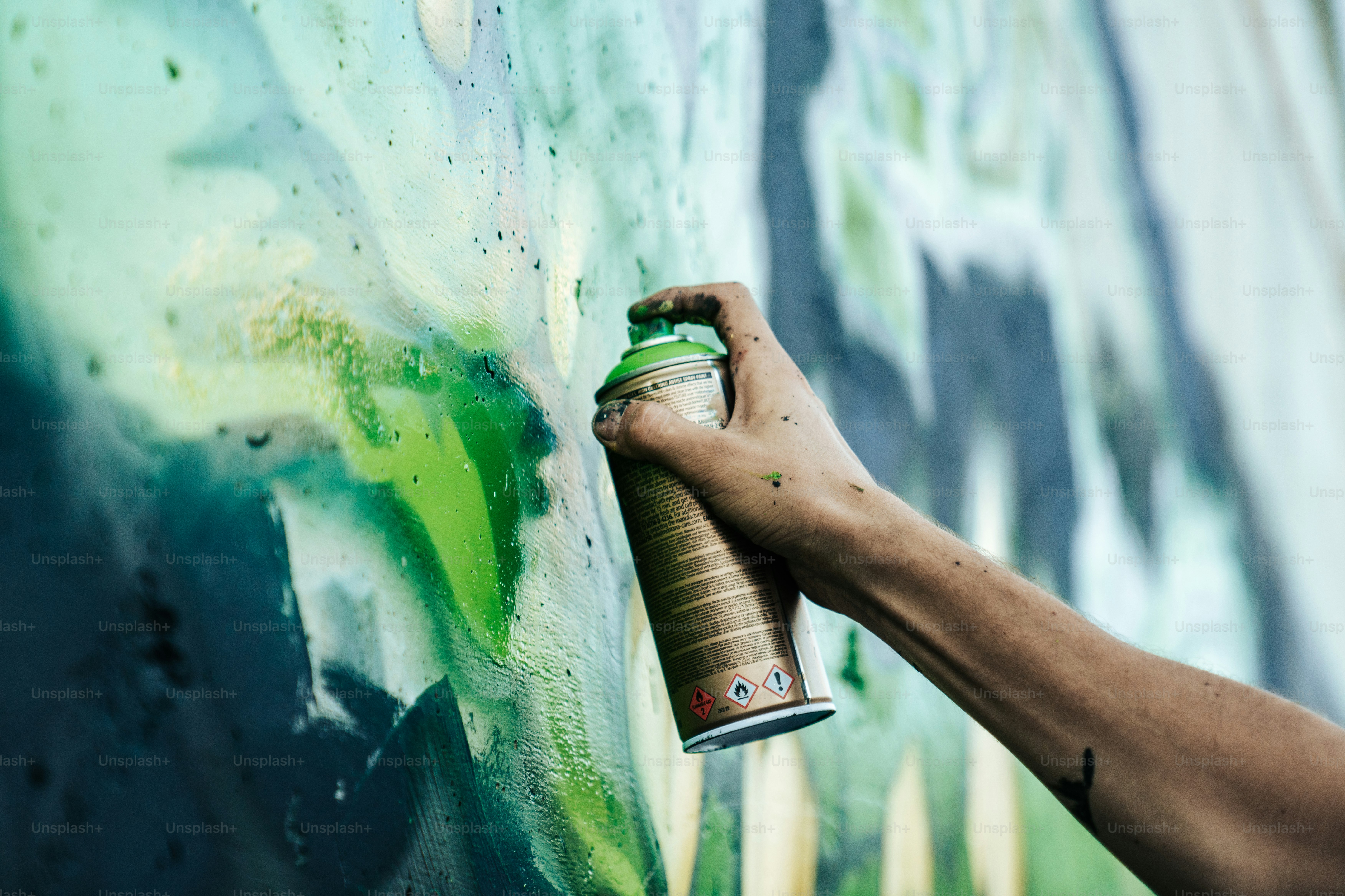 A person spray painting a wall with green paint photo – Street art ...