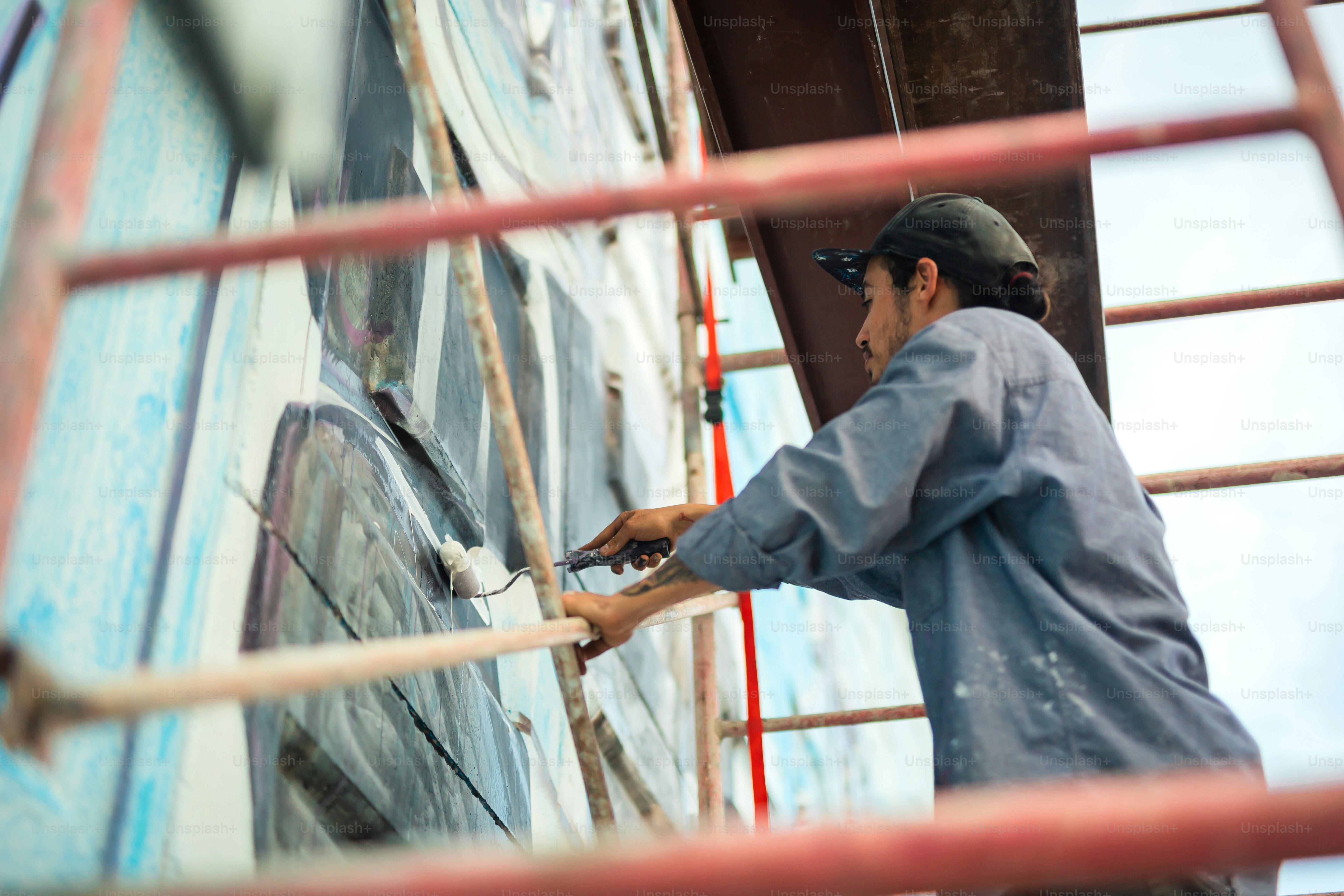 A man painting a mural on the side of a building photo – Painting Image ...