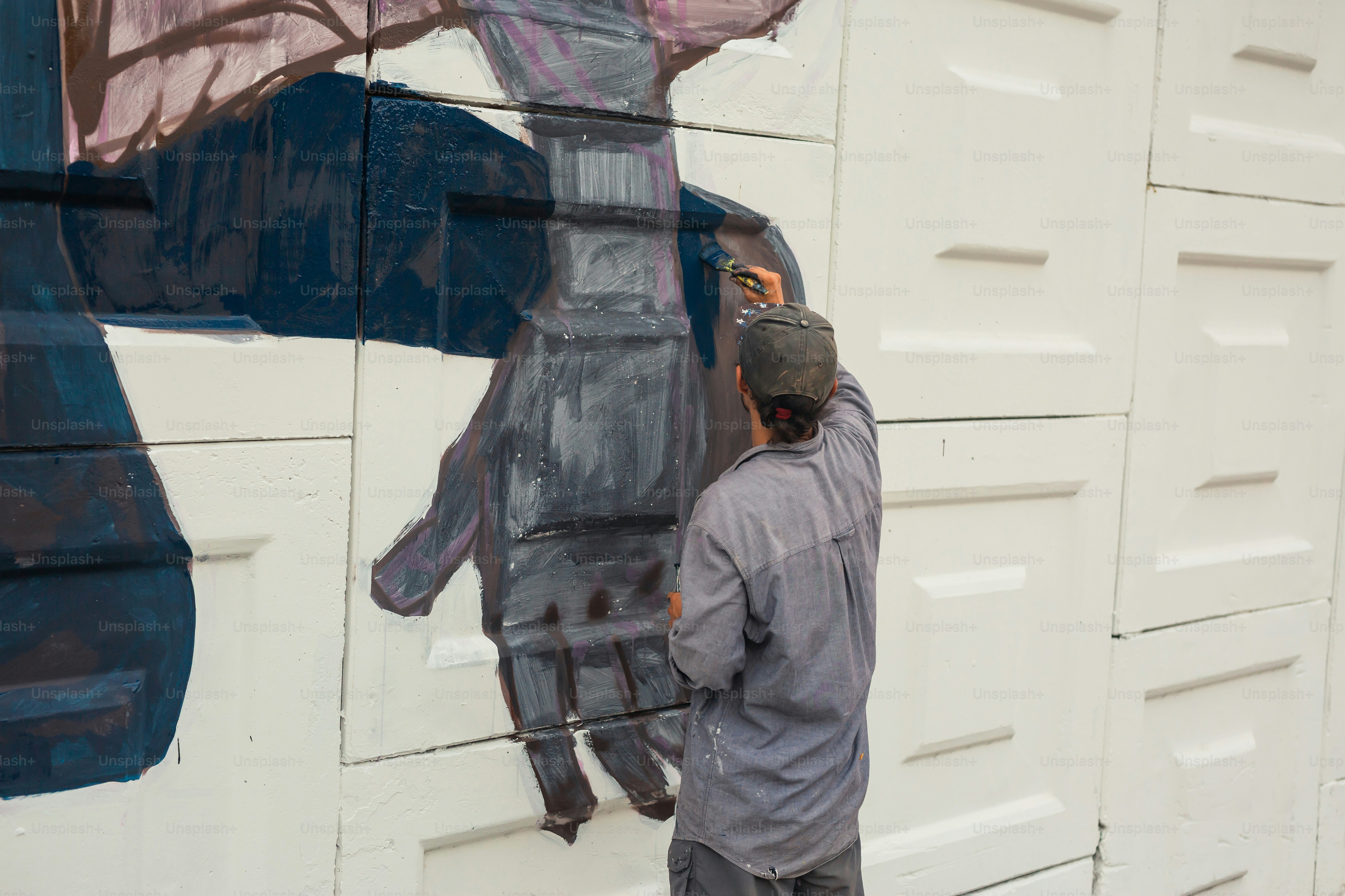 A man painting a mural on the side of a building photo – Mural Image on ...