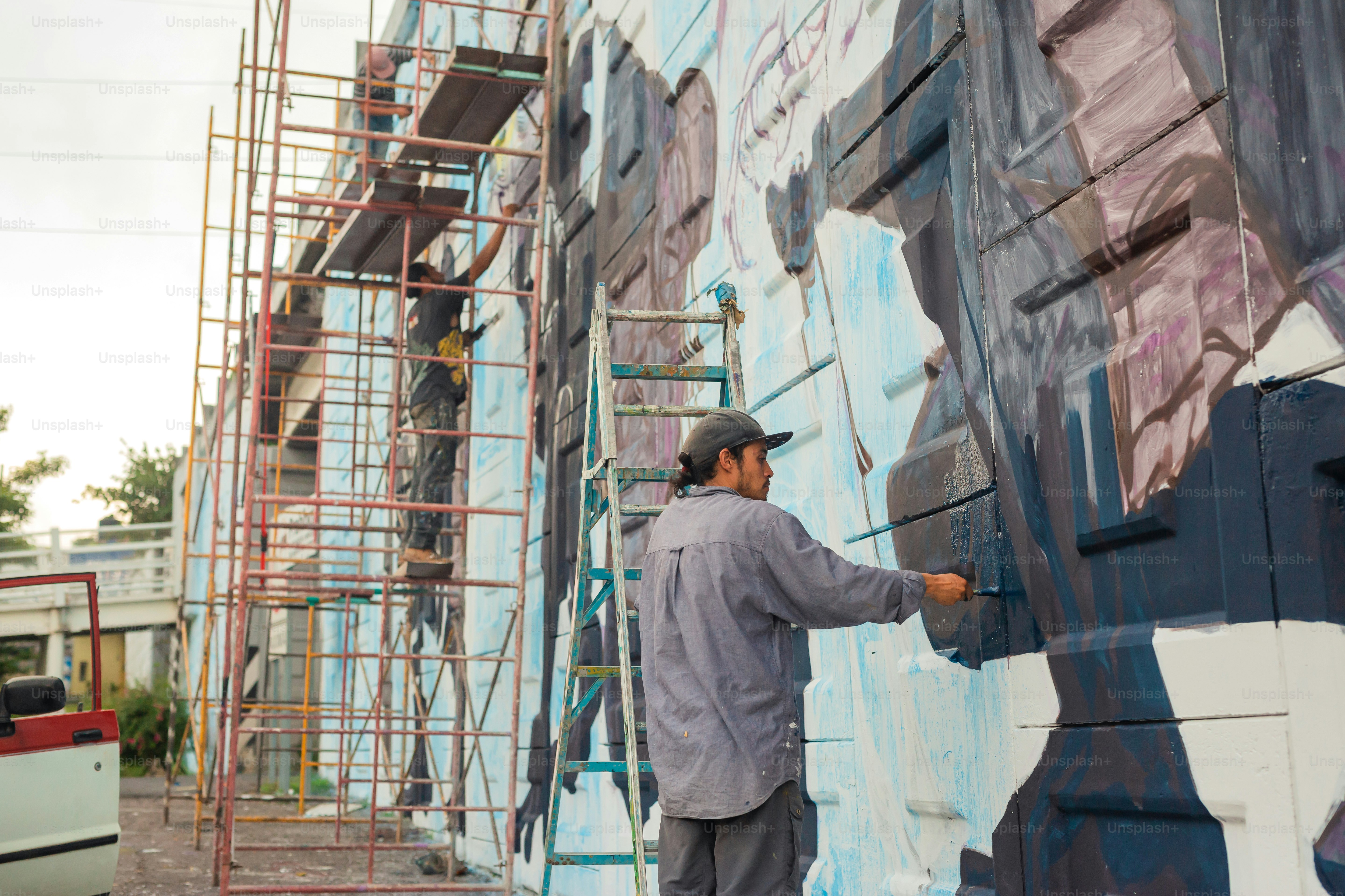 A man painting a mural on the side of a building photo – Mural Image on ...
