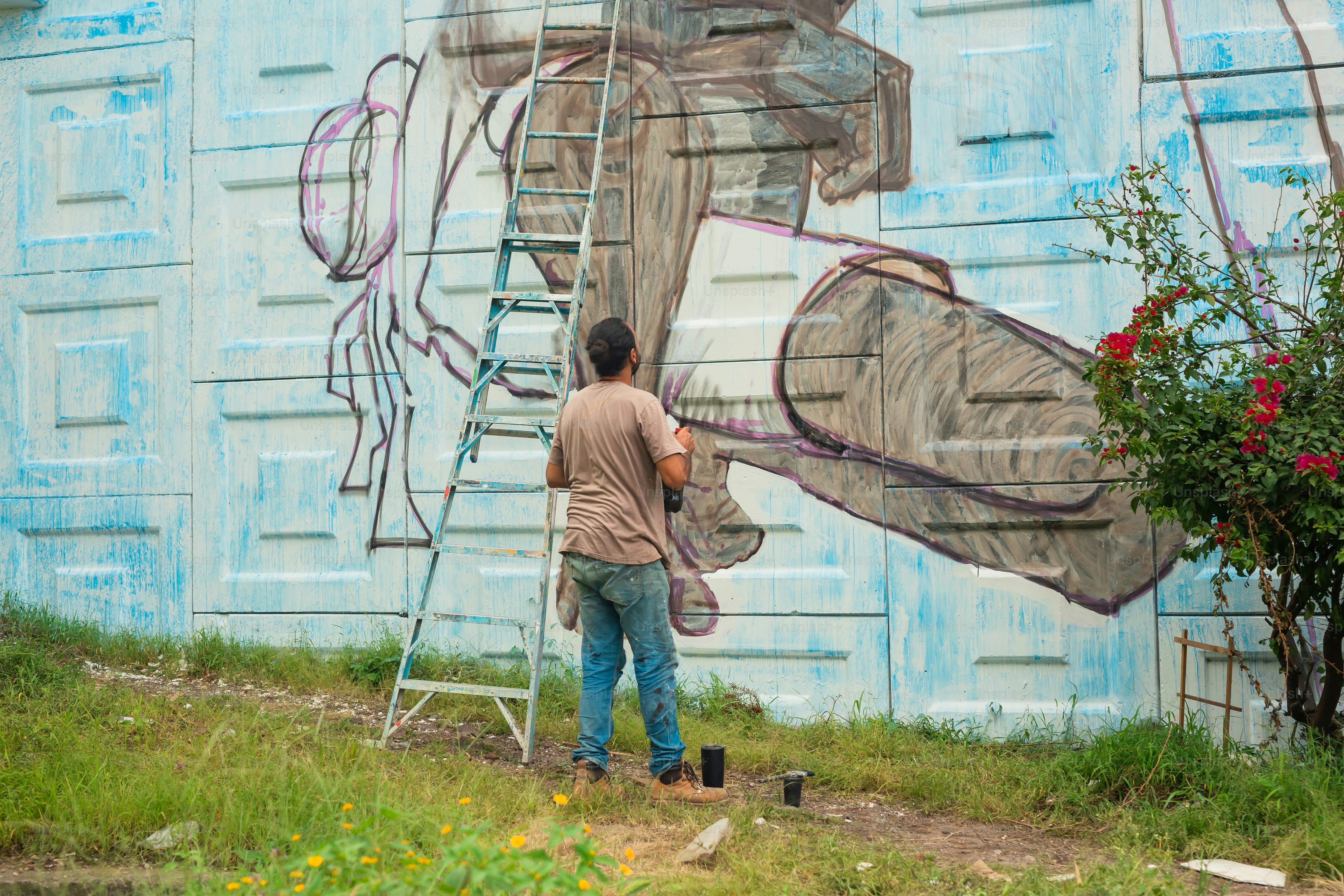 A man painting a mural on the side of a building photo – Street art ...
