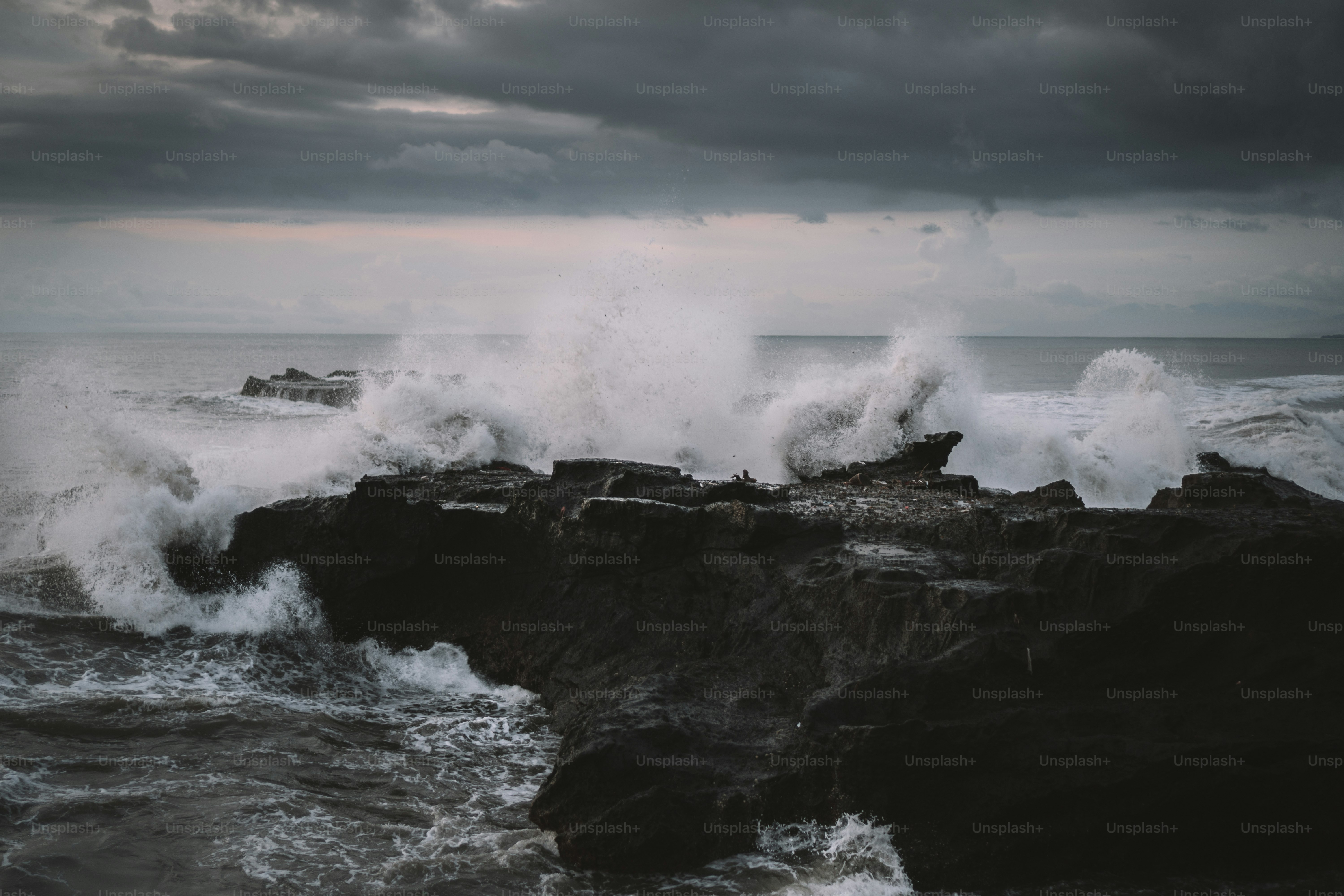 A large wave crashes against a rocky shore photo – Splash Image on Unsplash