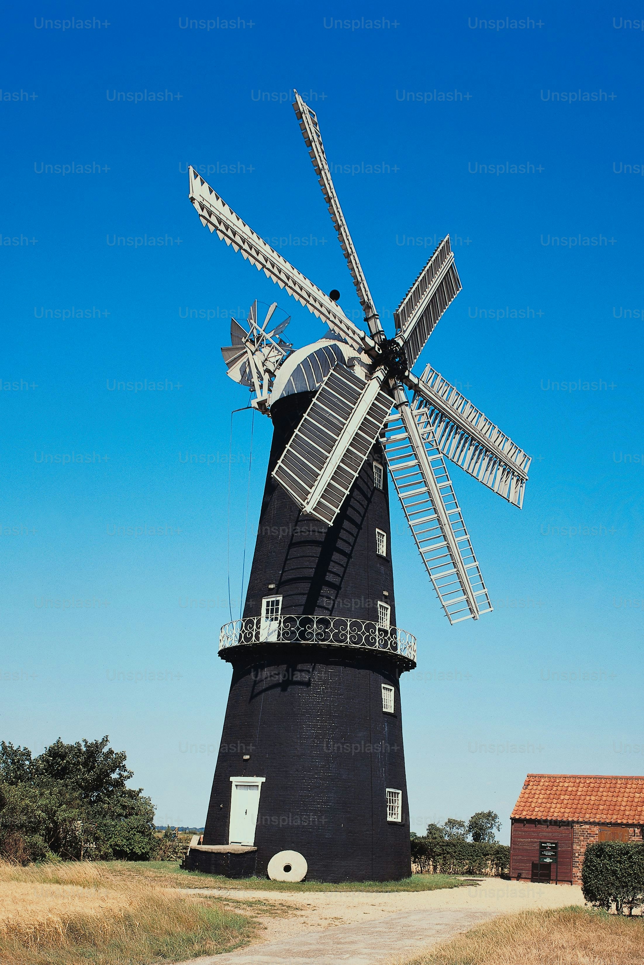 A windmill in a field with a blue sky in the background photo – England ...