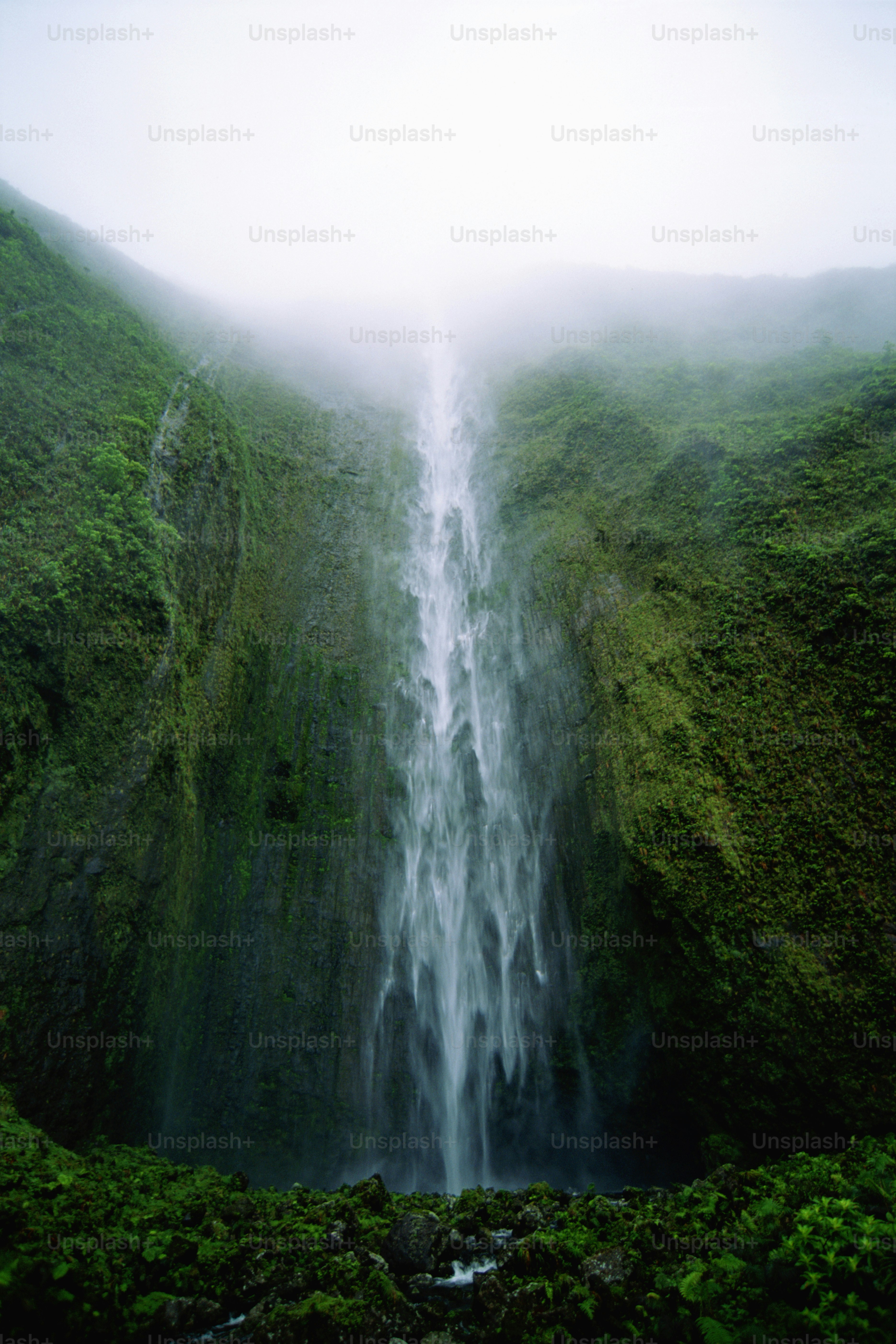 A very tall waterfall in the middle of a lush green hillside photo ...