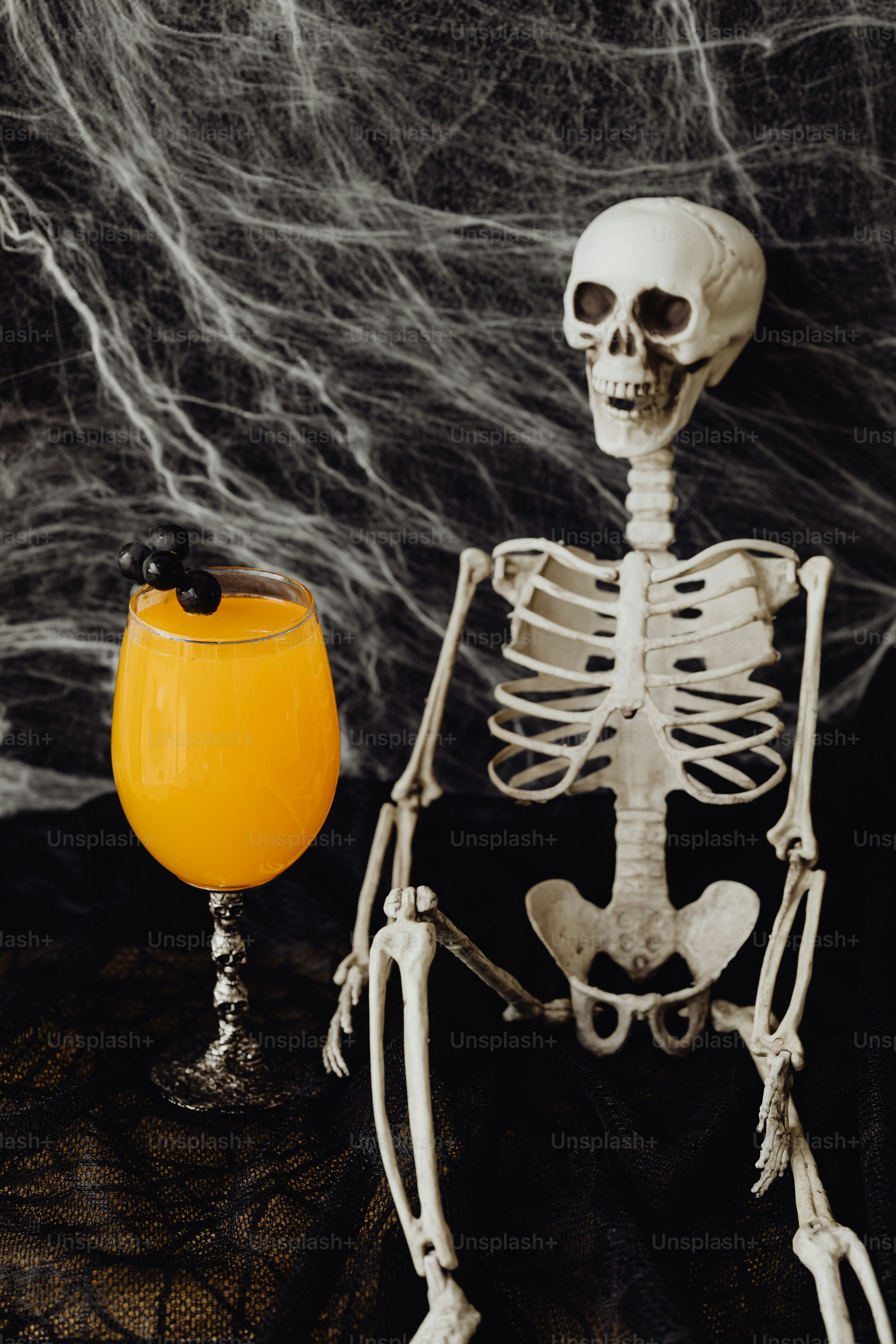 A skeleton sitting next to a glass of orange juice photo – Drinks Image ...