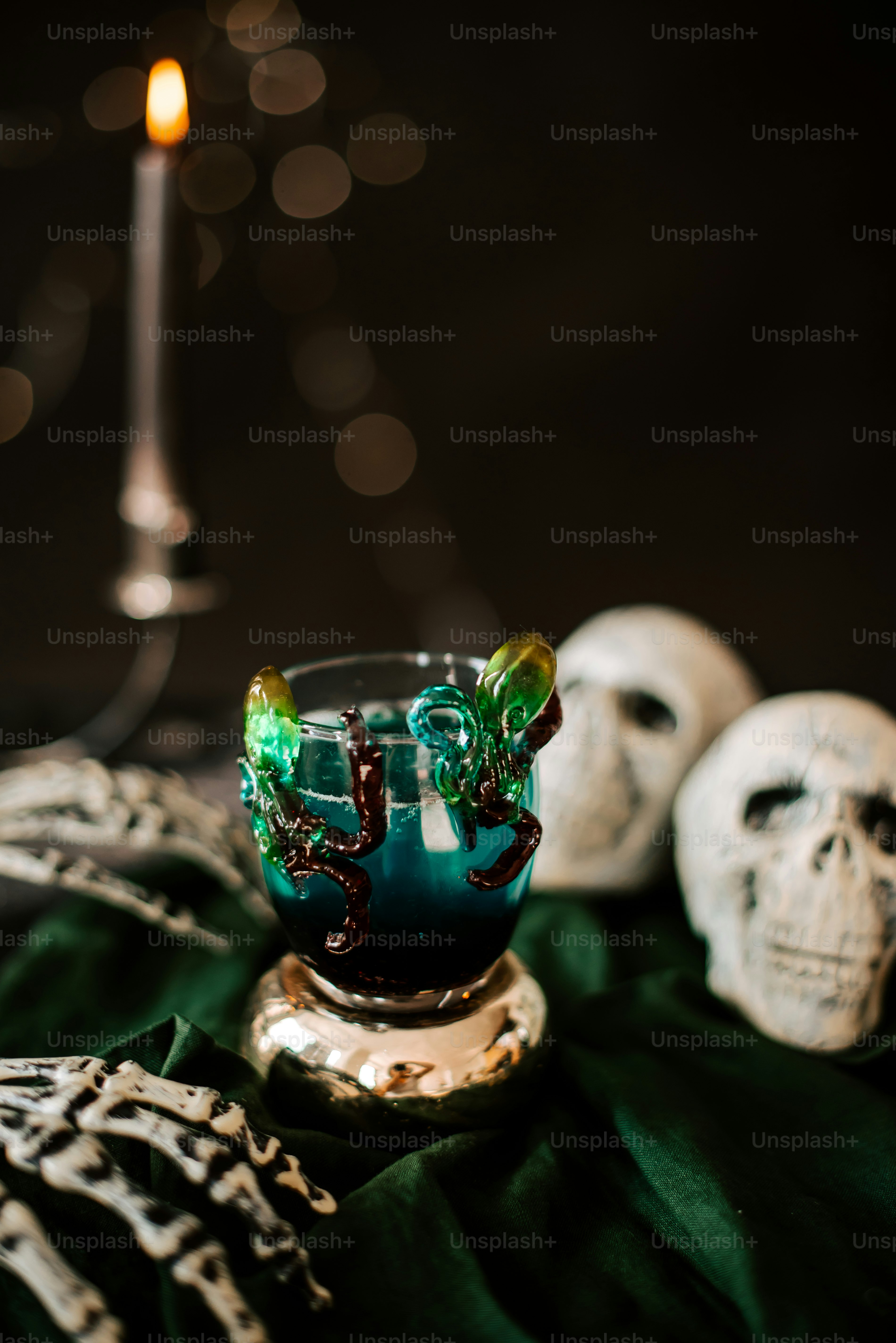 A glass with a green liquid in it next to two skulls photo – Halloween ...