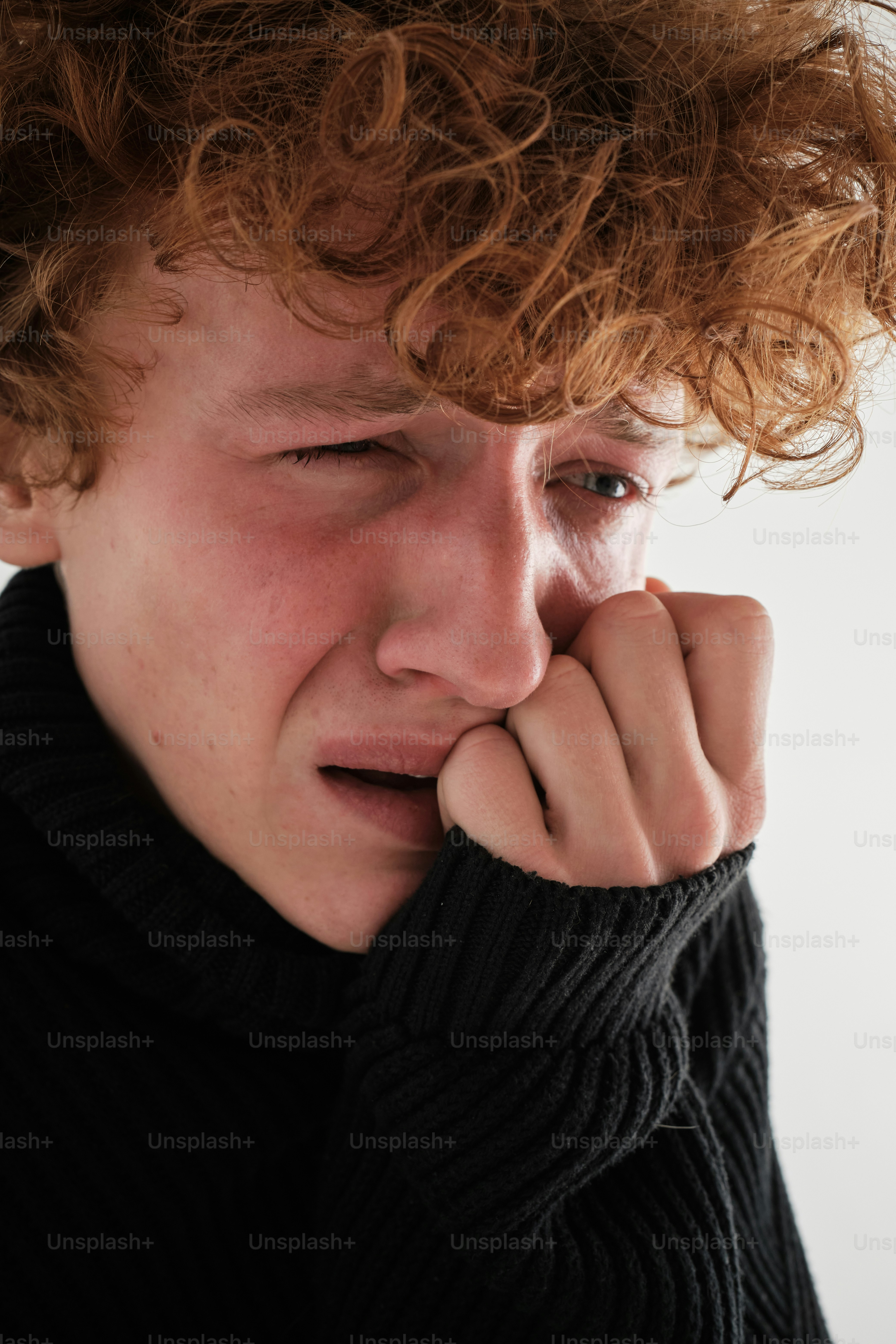 A young man with curly hair holding his hand to his face photo – Sad ...