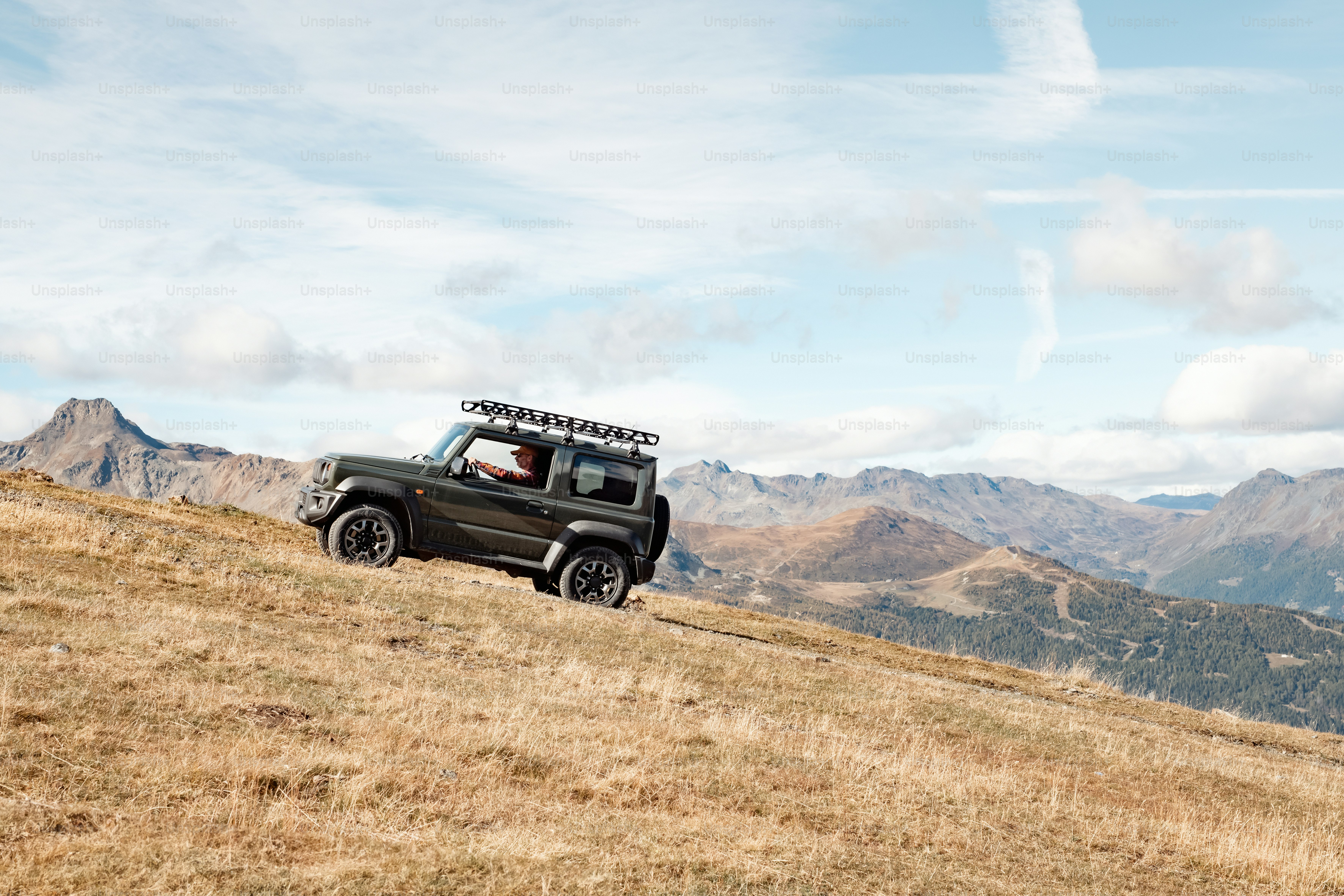 A jeep driving up a hill with mountains in the background photo ...