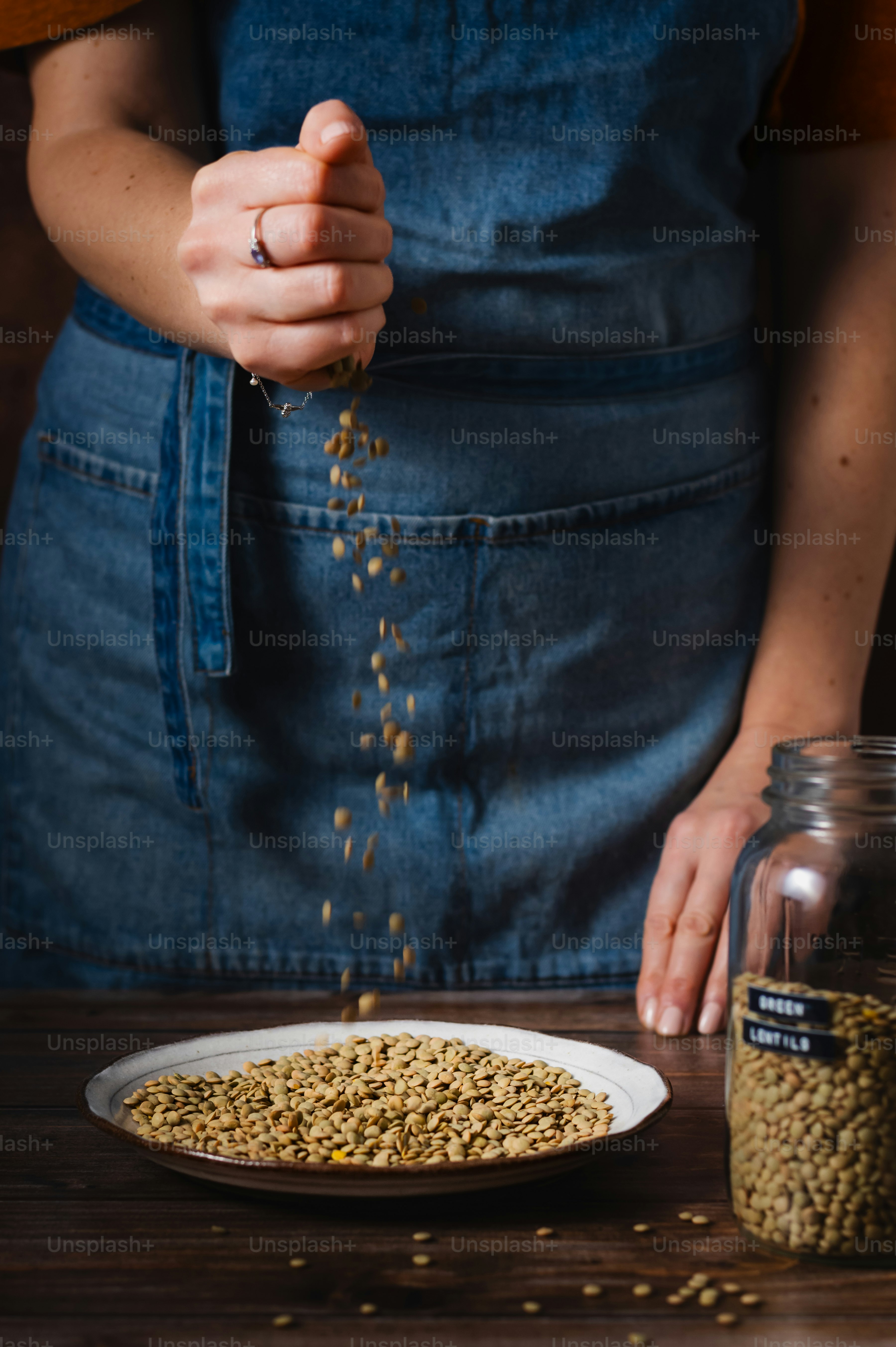 A person in an apron sprinkling seeds on a plate photo – Green lentils ...