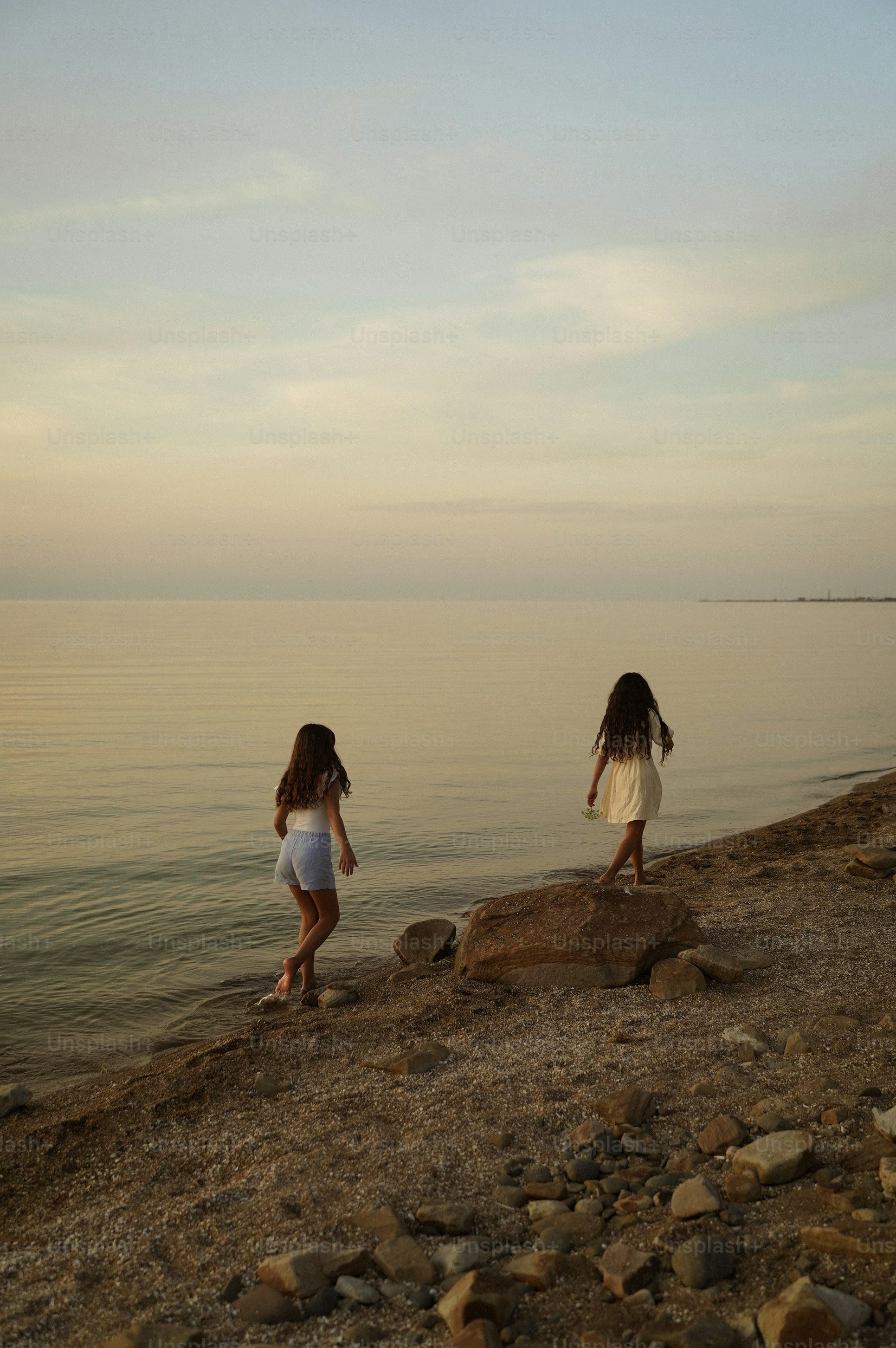 Two young girls walking along the shore of a body of water photo ...