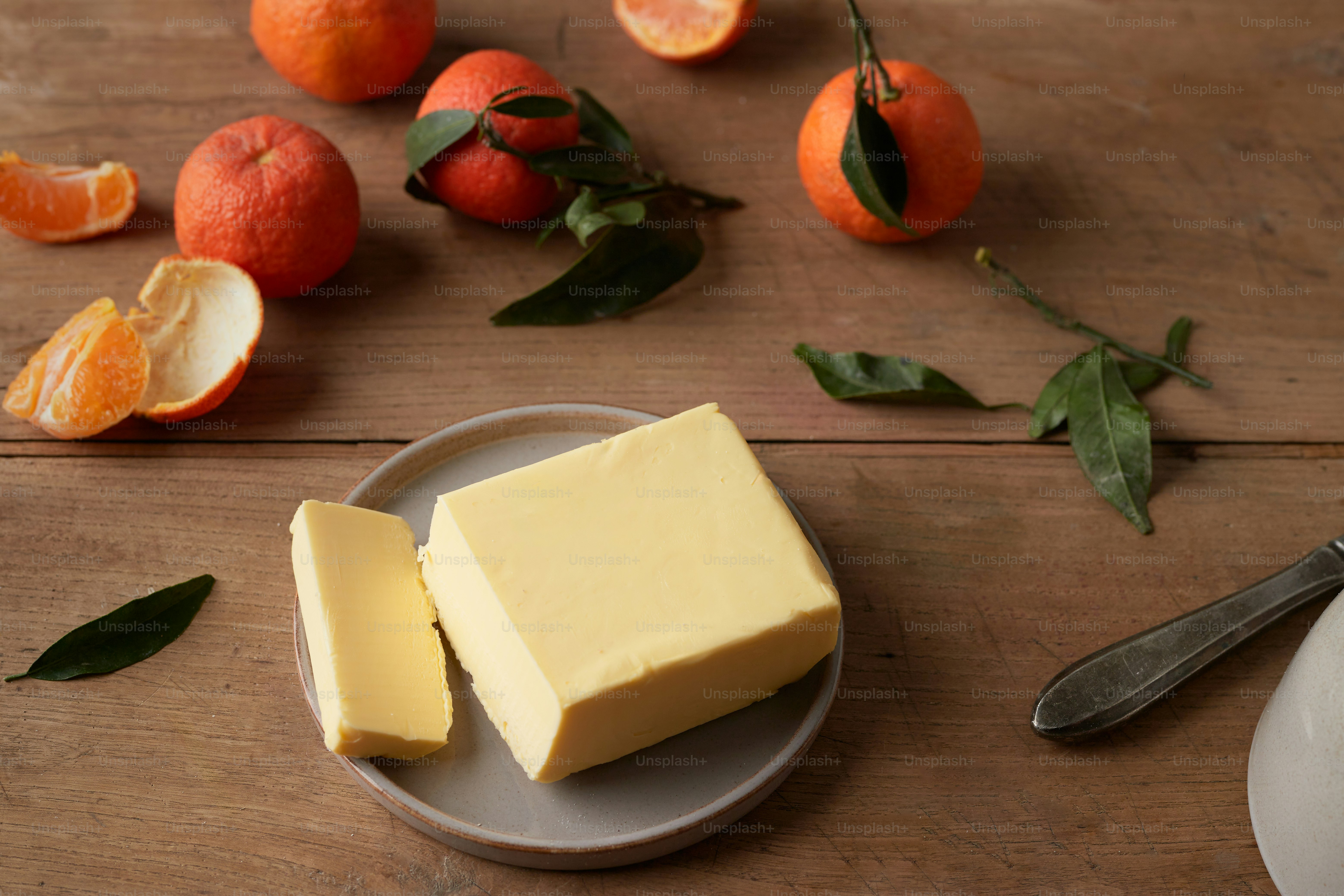 A piece of butter sits on a plate next to some oranges photo – Butter ...