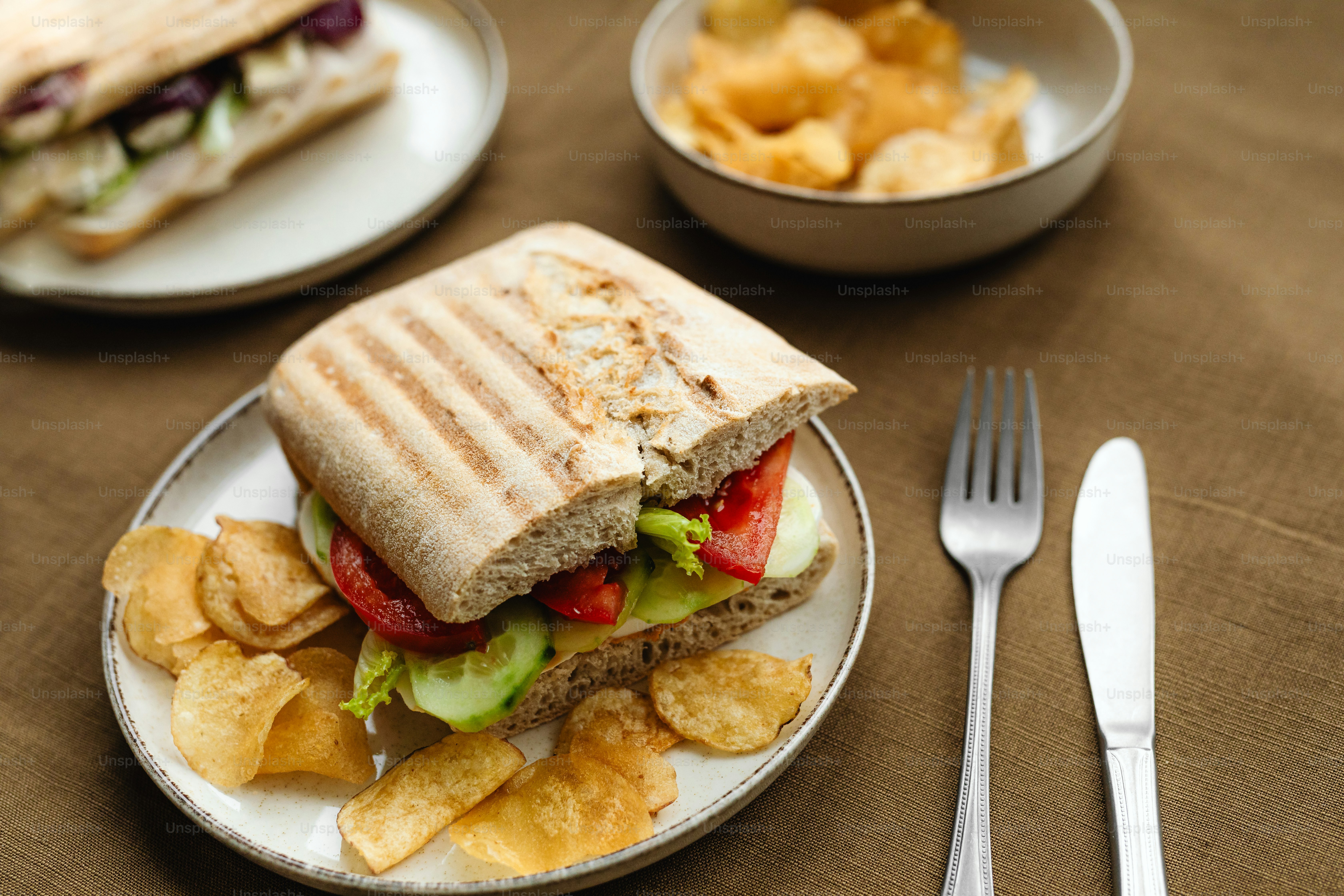 Two plates with sandwiches and chips on a table photo – Panini Image on ...