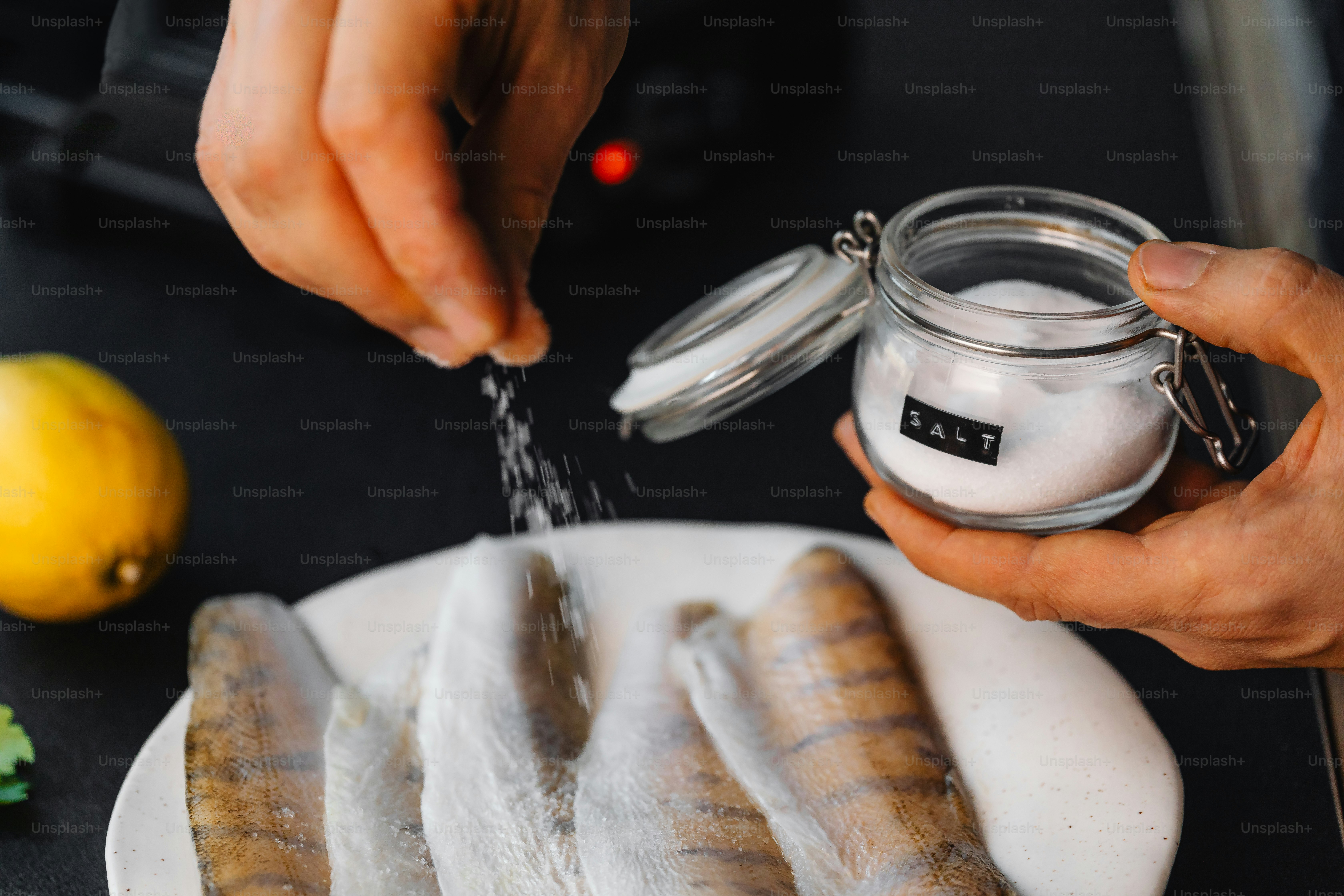 A person sprinkling salt onto fish on a plate photo – Grilled fish ...