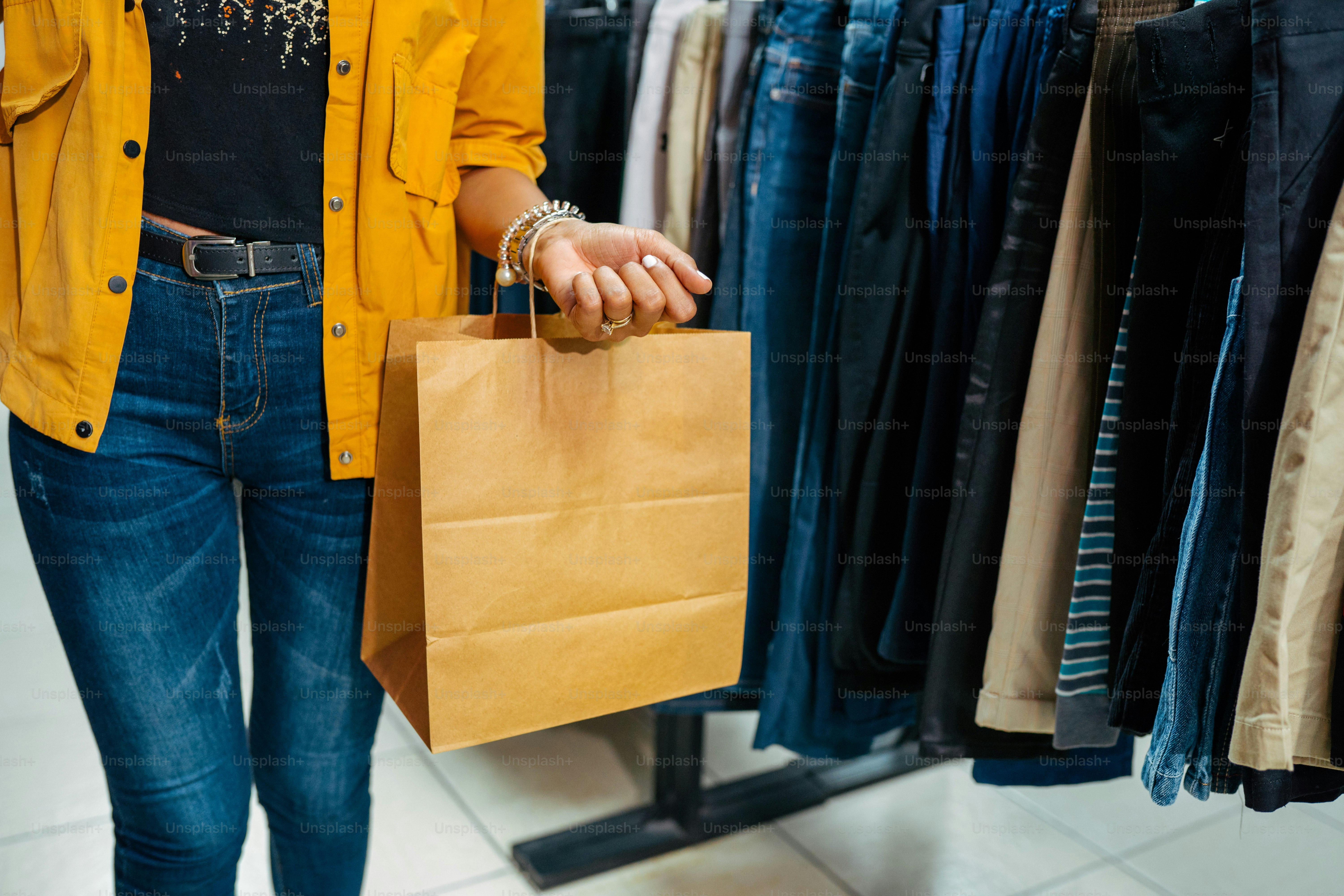 A woman holding a shopping bag in front of a rack of clothes photo ...