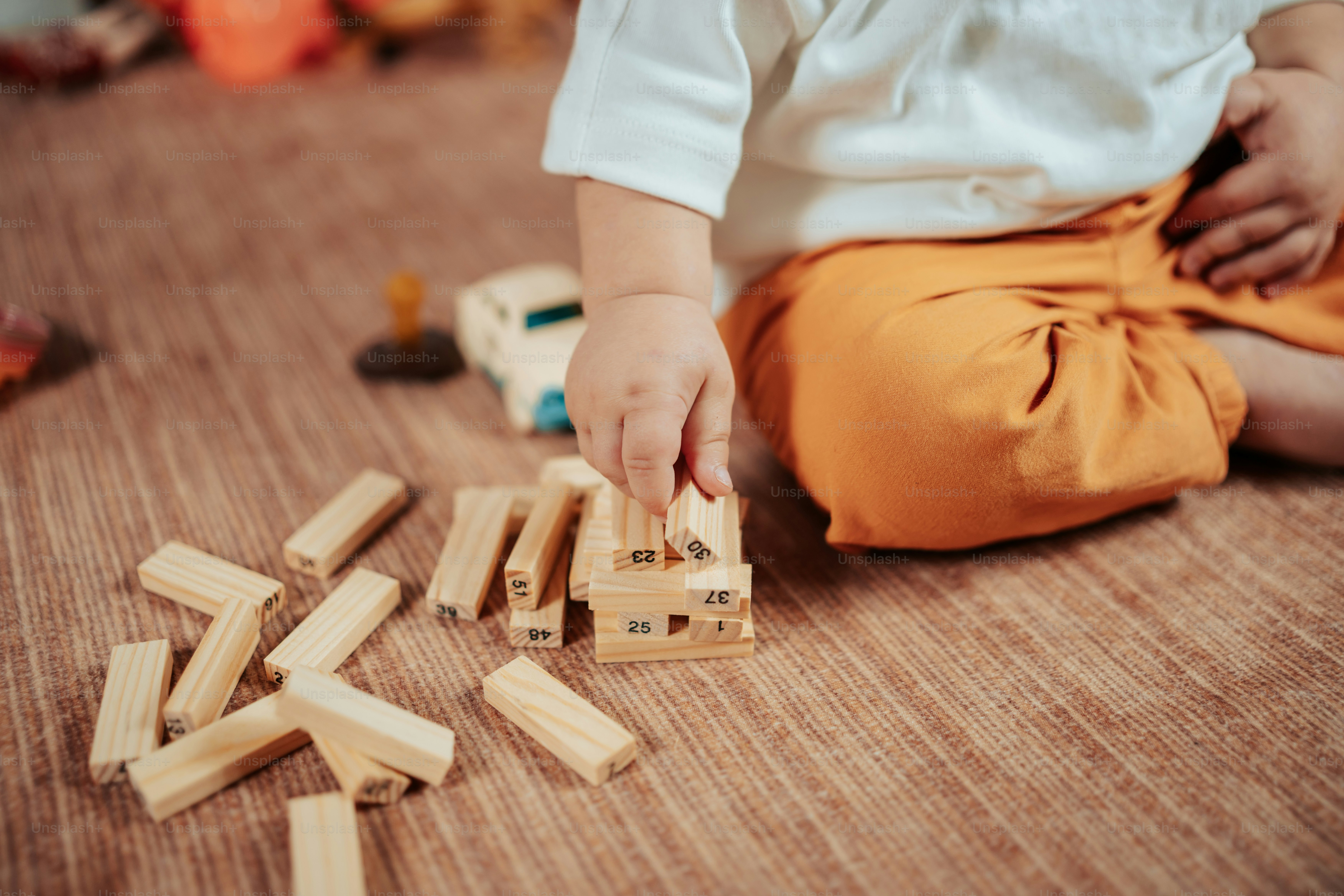 A baby playing with wooden blocks on the floor photo – Wooden toys ...