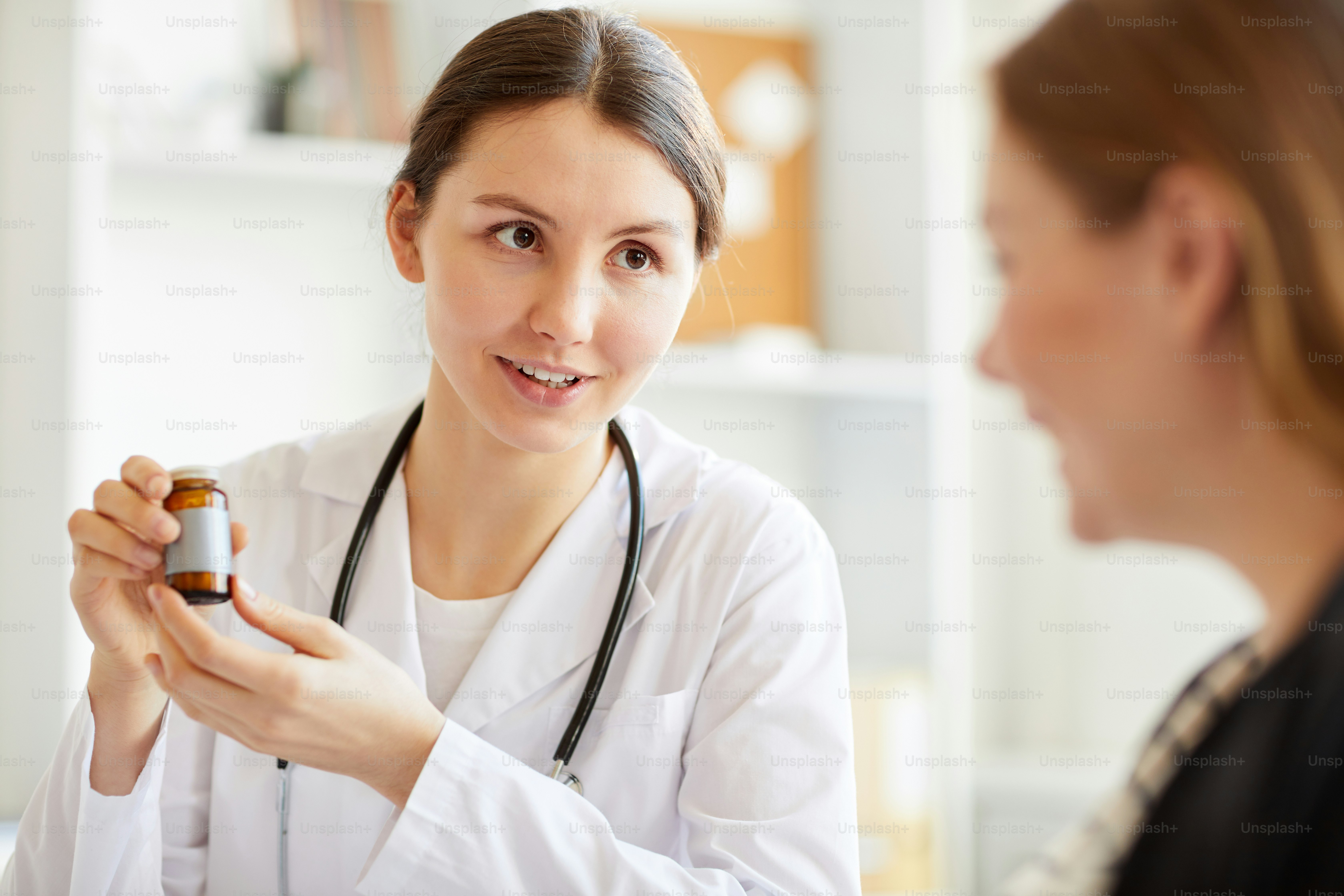 Portrait of female obstetrician showing vitamins to pregnant woman ...