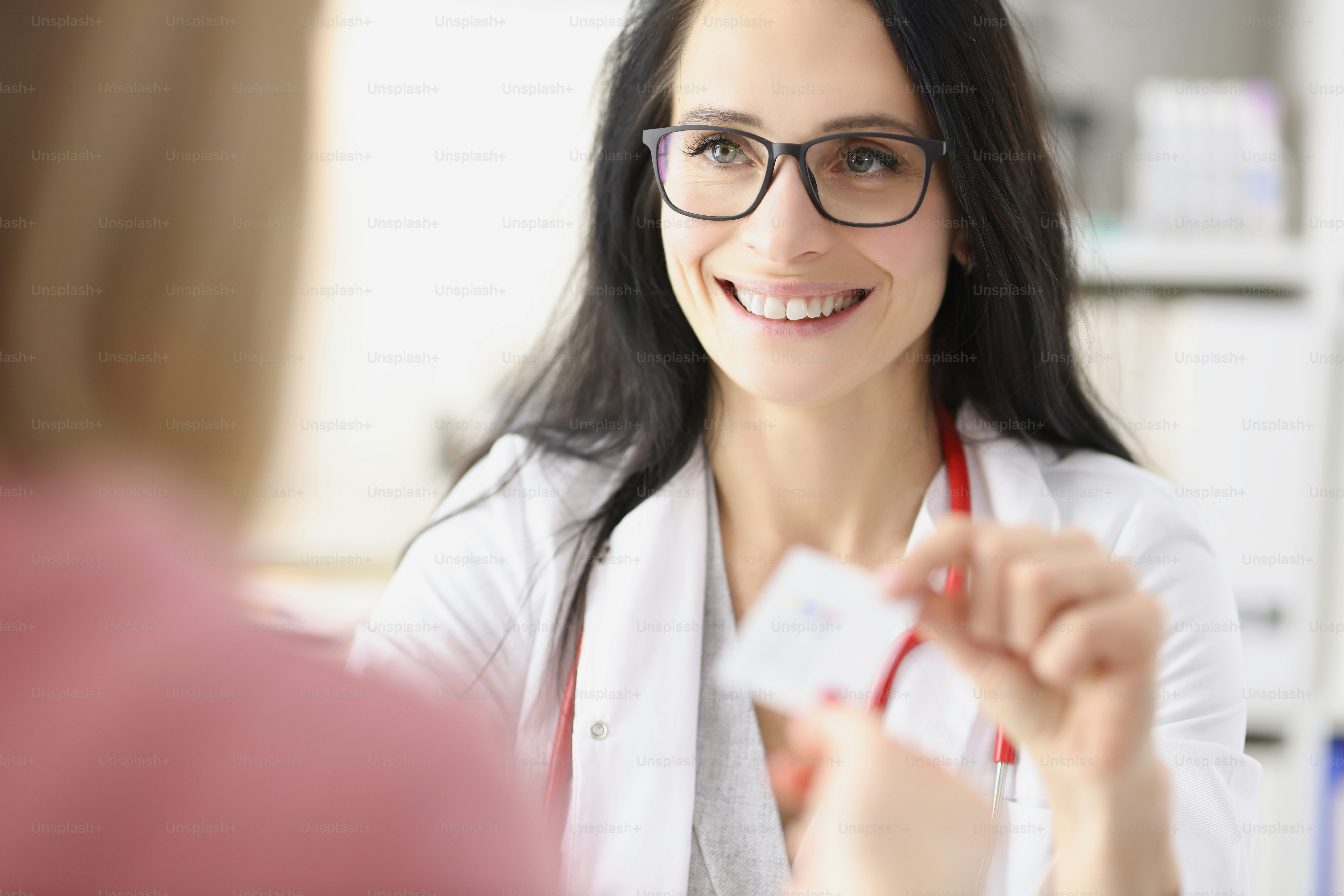 Smiling female doctor giving business card to patient at reception in ...