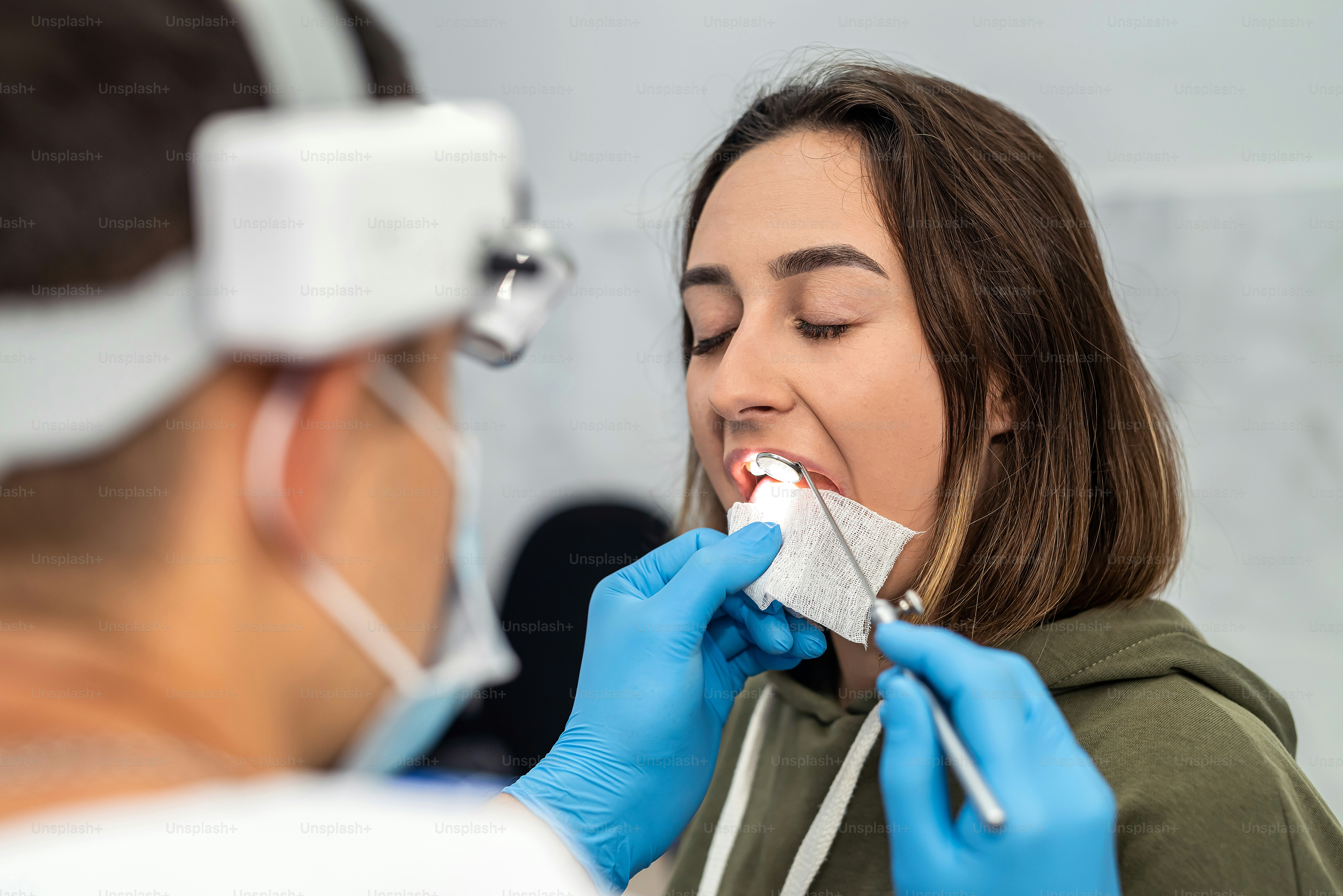 An ENT specialist in a mask examines a patient's sore throat in the ...