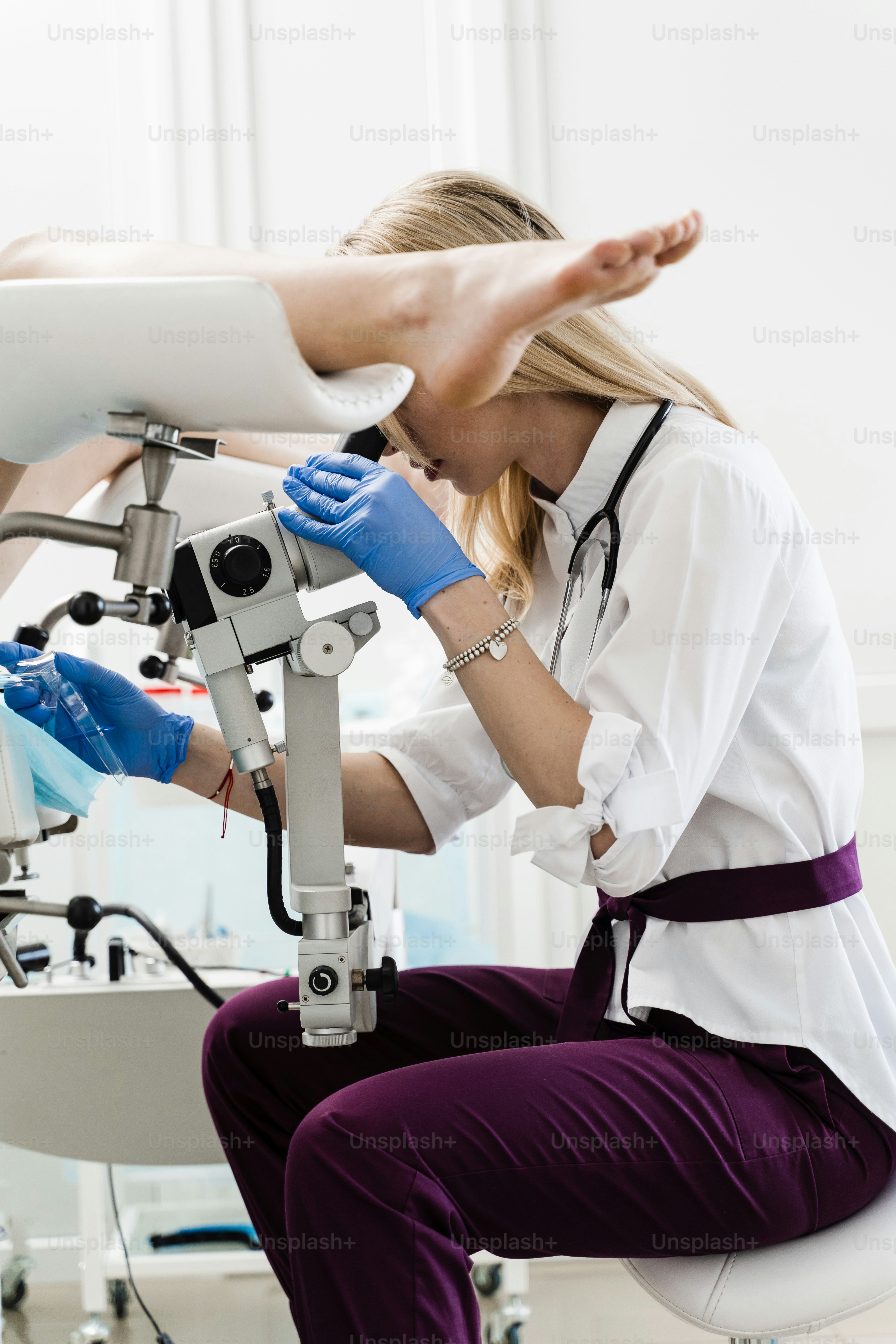 Gynecologist is looking in colposcope for detail examination of disease ...