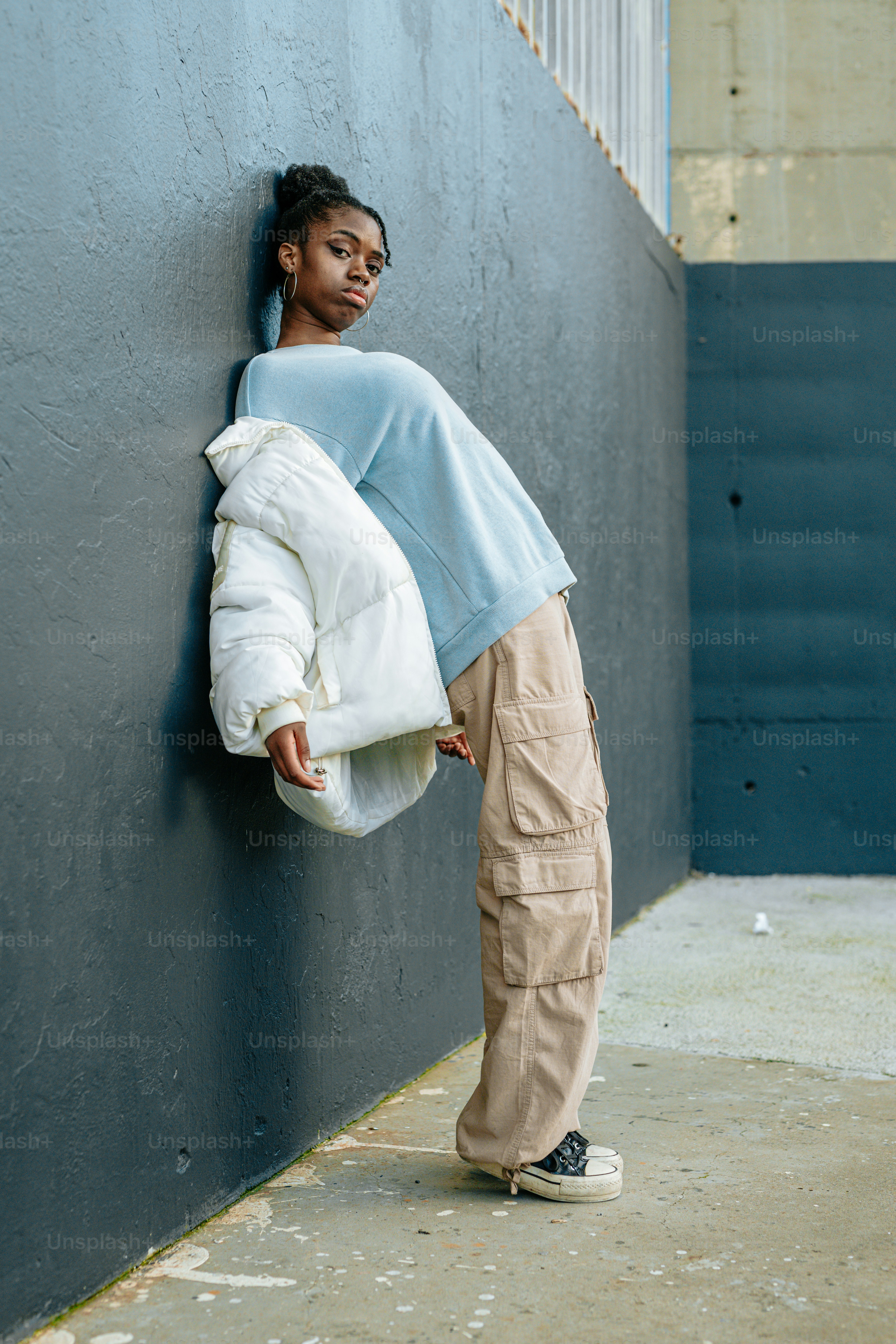 A woman leaning against a wall with a white jacket on photo – Style ...