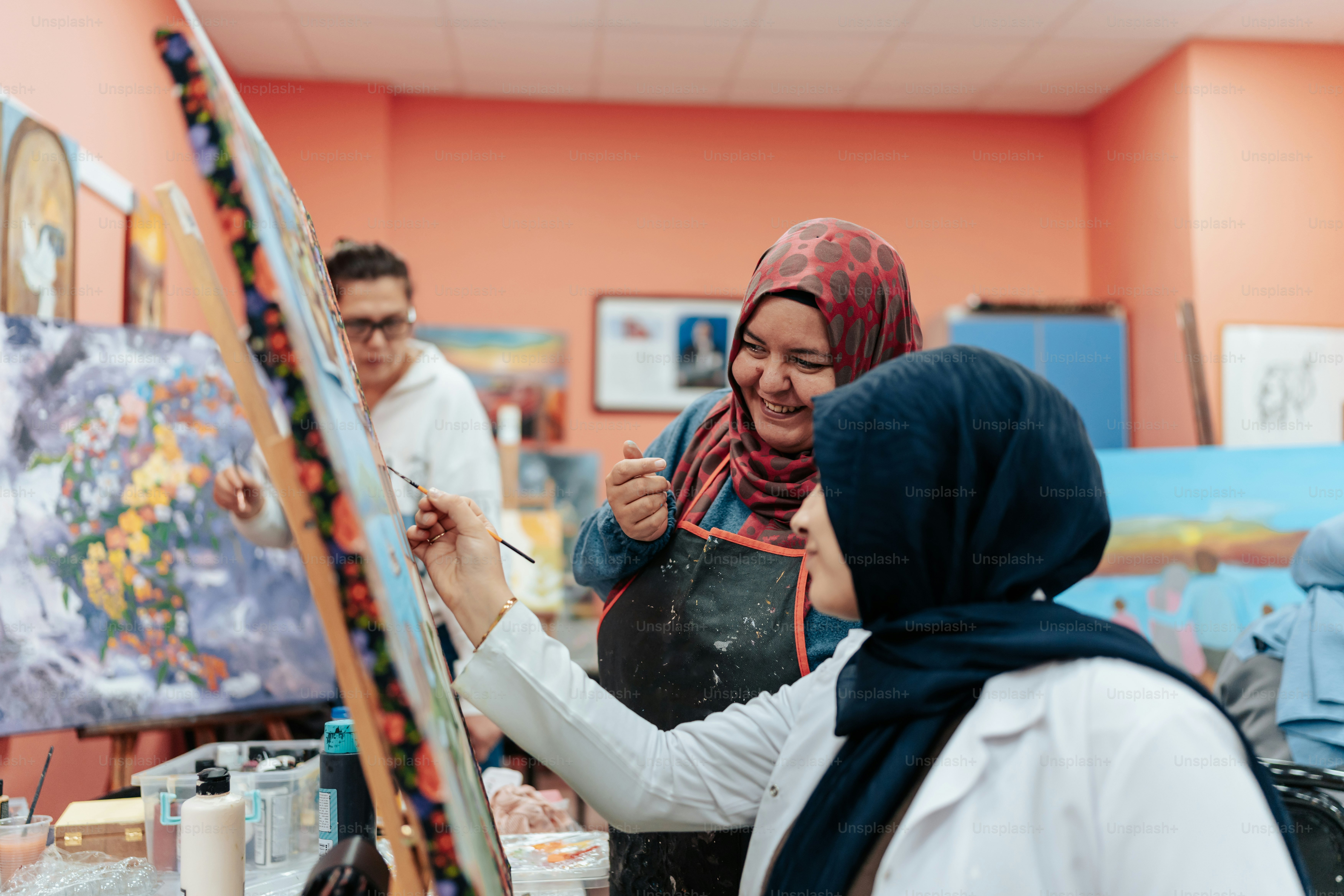 A group of people standing around a painting on a easel photo ...